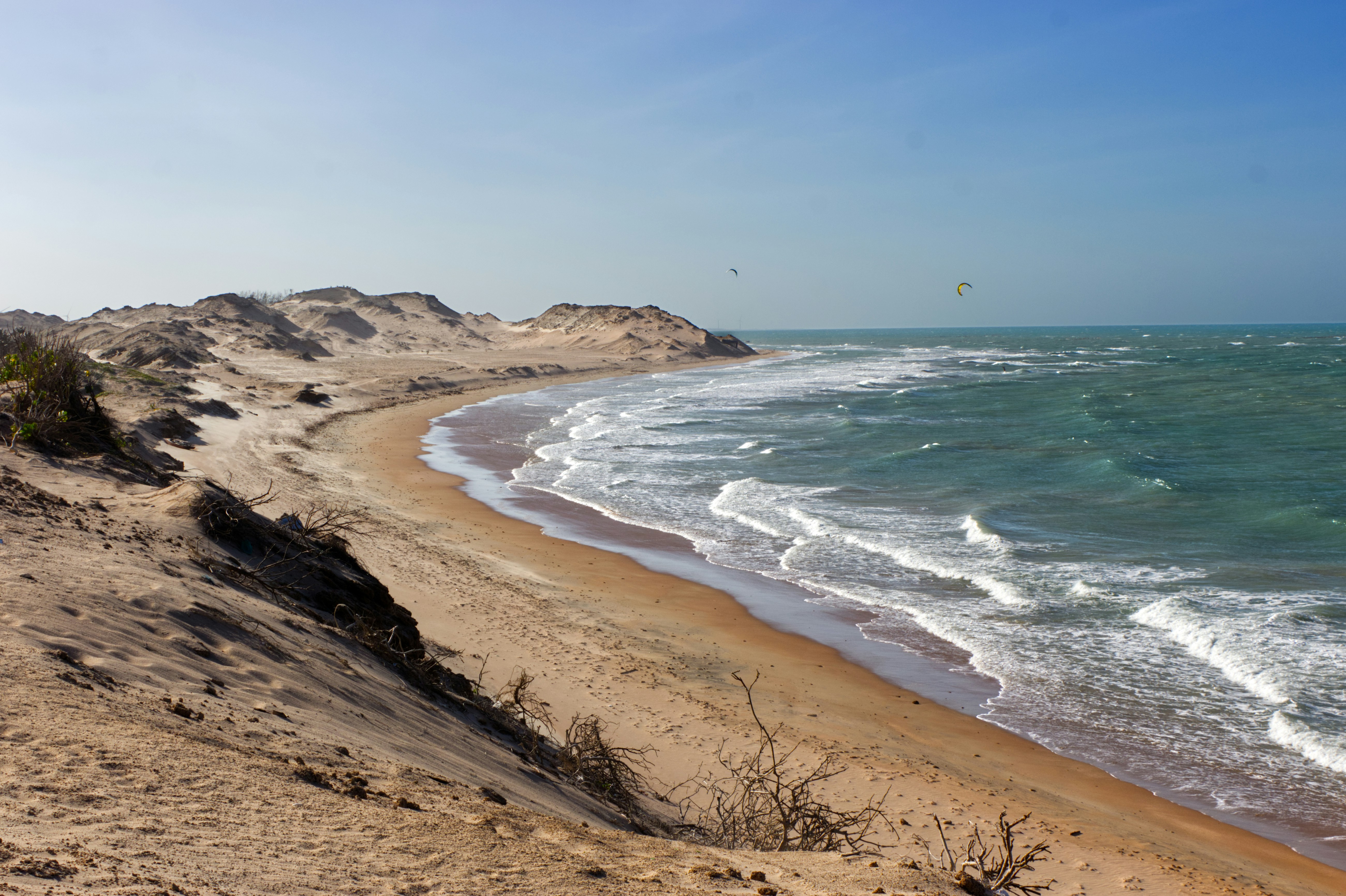 Rolling waves meet a sandy beach under a clear blue sky.