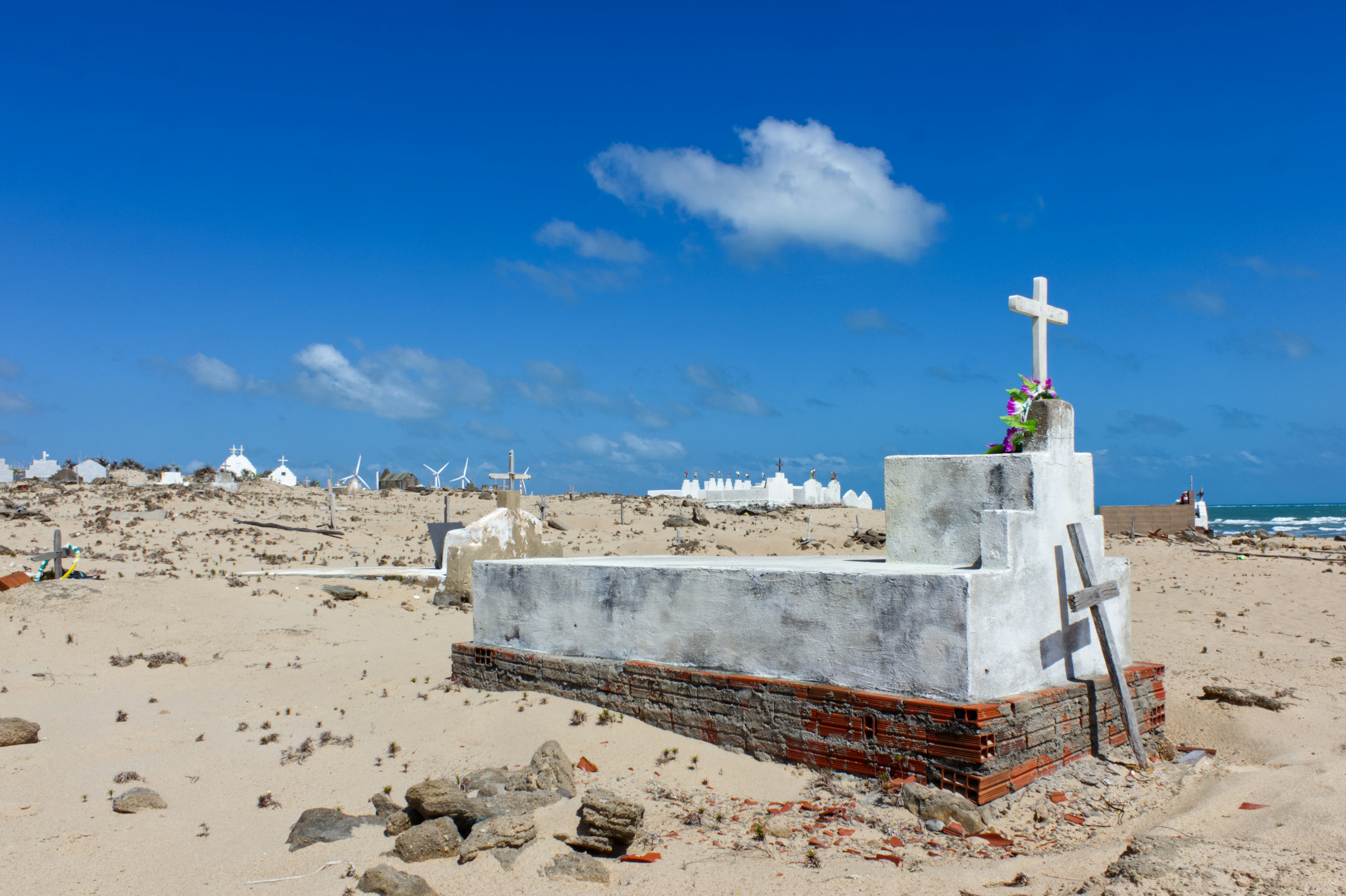 White grave under a clear blue sky on a sandy beach with scattered stones.
