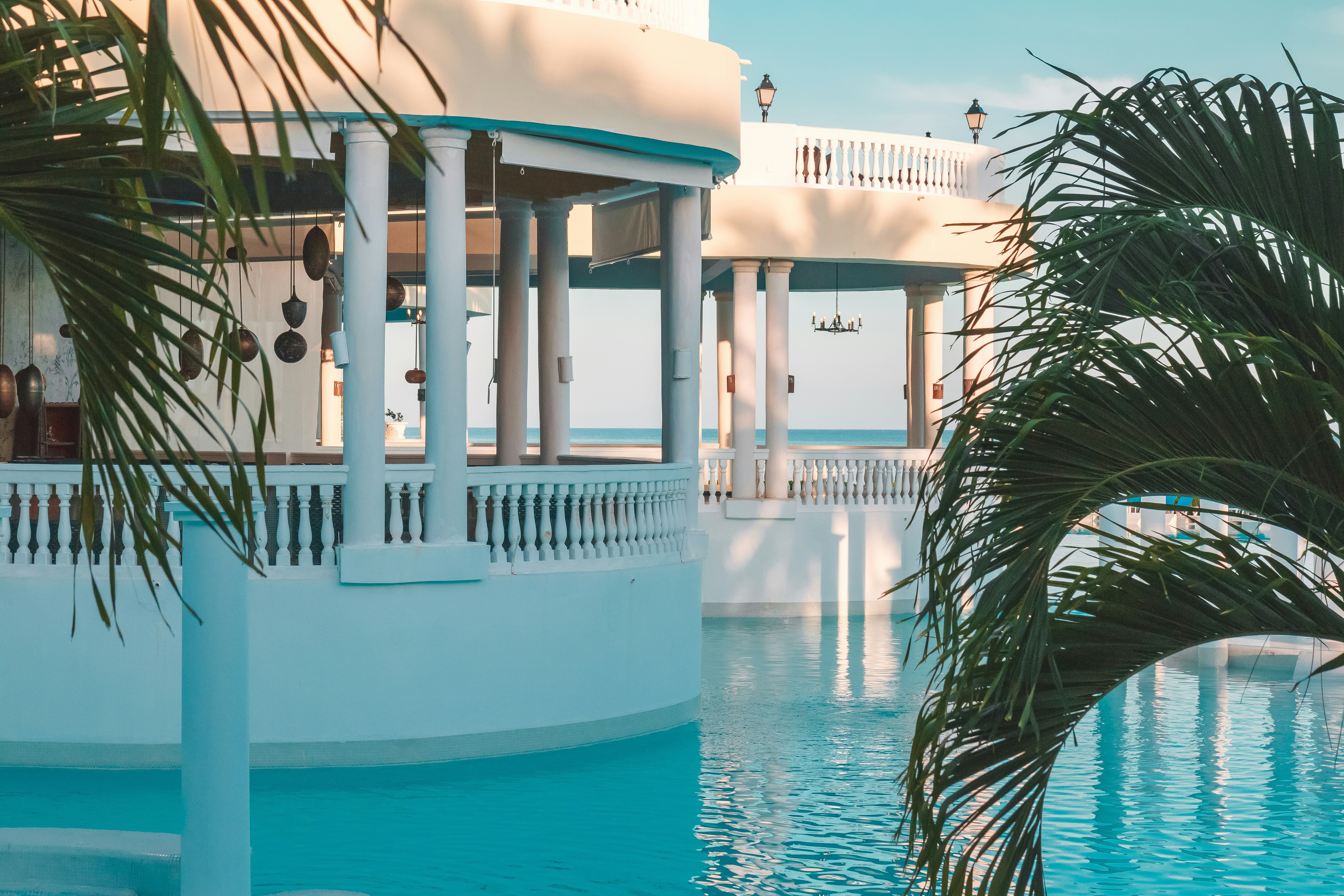Elegant seaside architecture reflected in a serene pool framed by lush palm leaves.