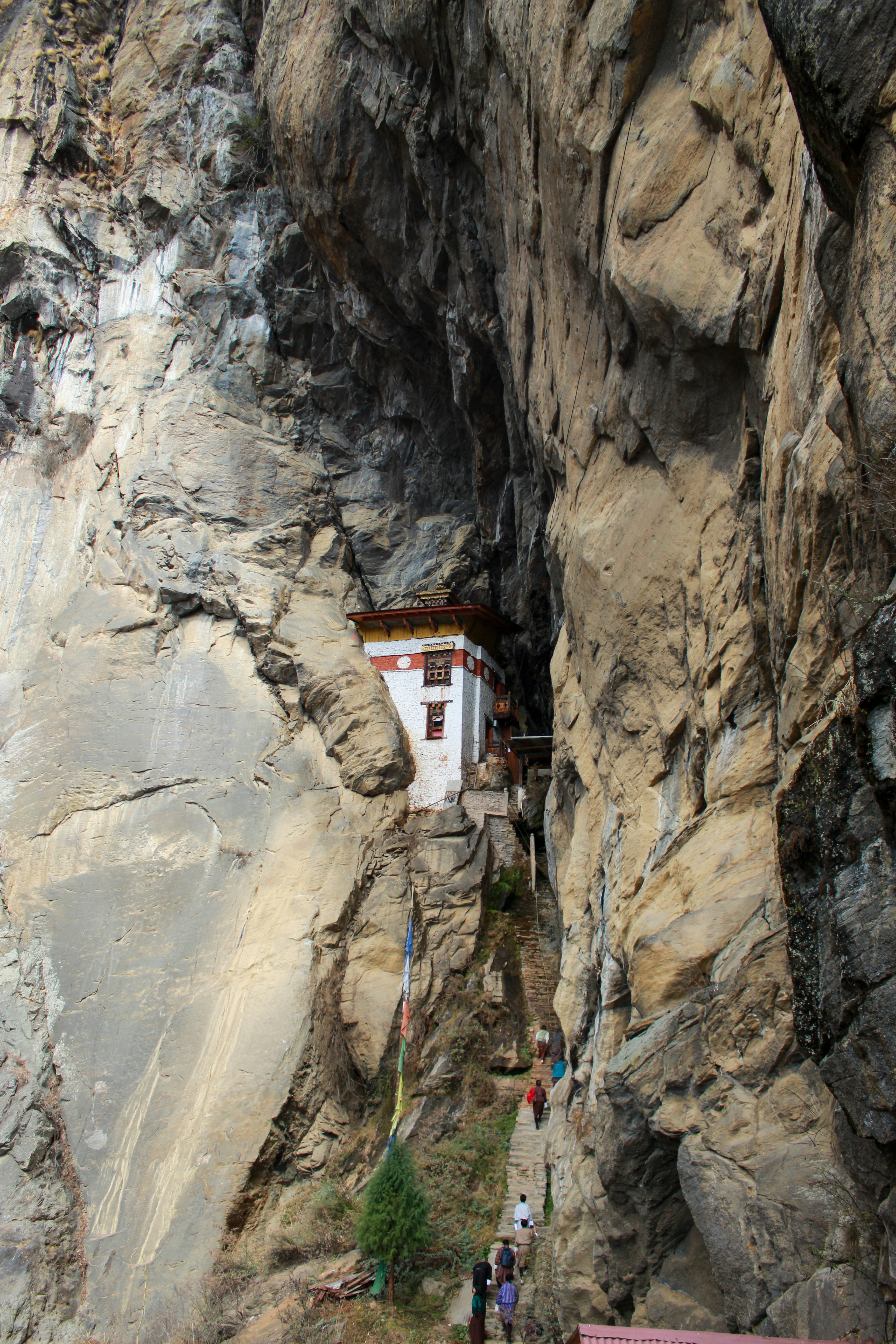 White monastery built into towering rocky cliffs with narrow path below.