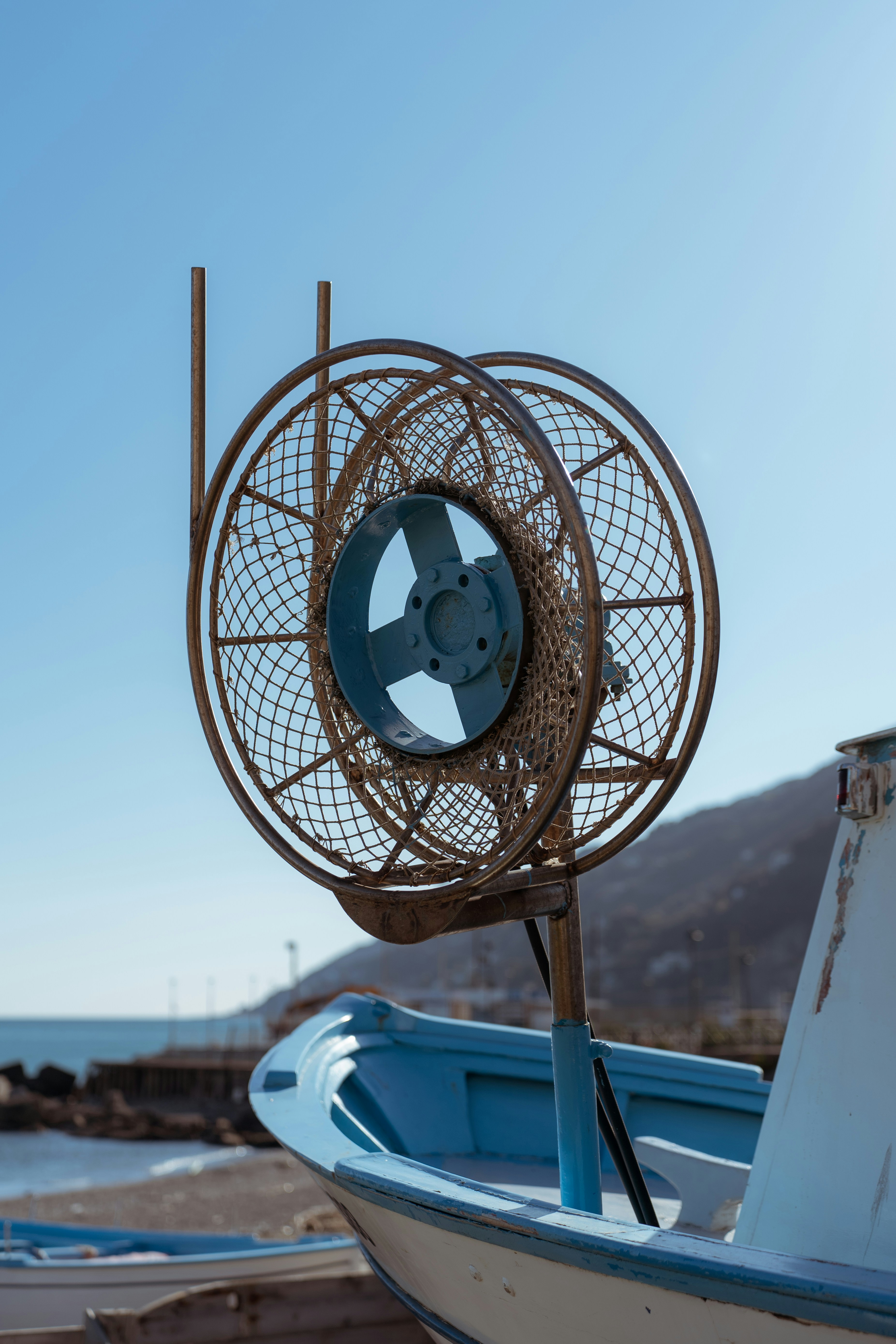 Circular Rust: A Net Spool Framing a Weathered Blue Boat by the Sea