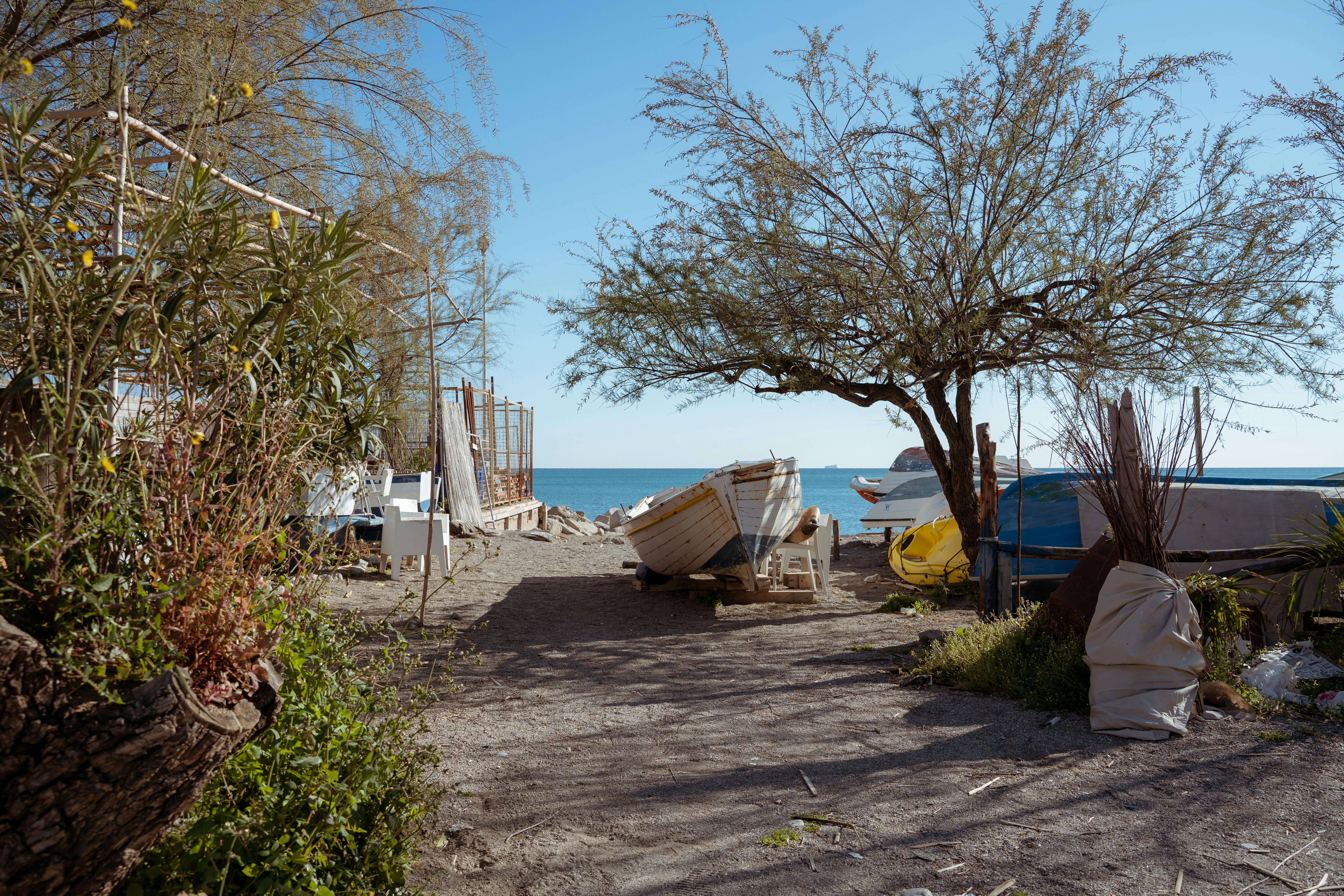 Rustic boatyard with scattered tools and a view of the sea under a clear blue sky.