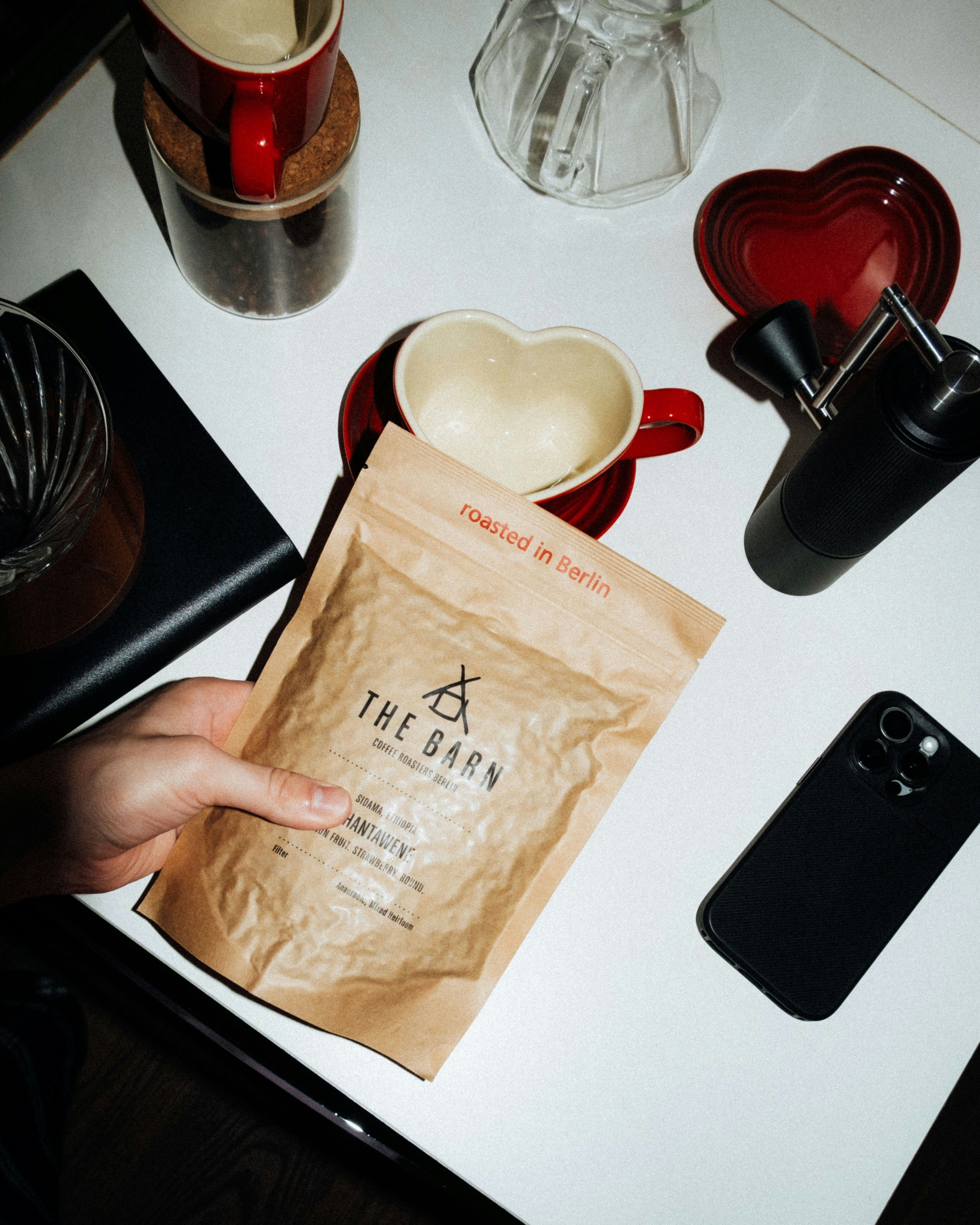 Coffee setup with a heart-shaped mug, coffee bag, and brewing tools on a white table.