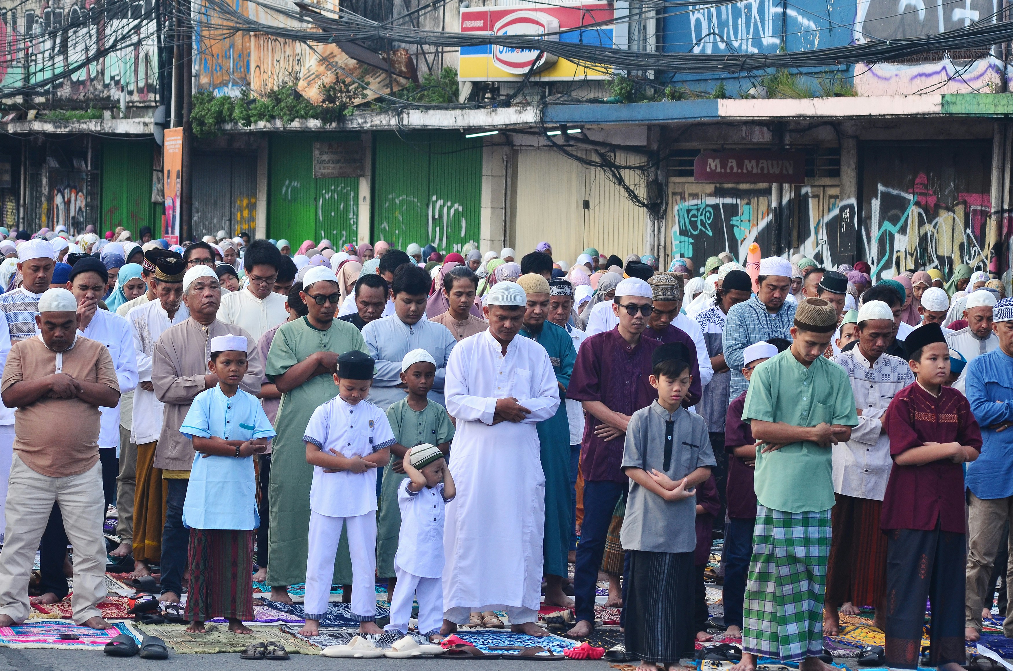 People gathered for Eid Mubarak prayers on a Jakarta street, surrounded by urban scenery.