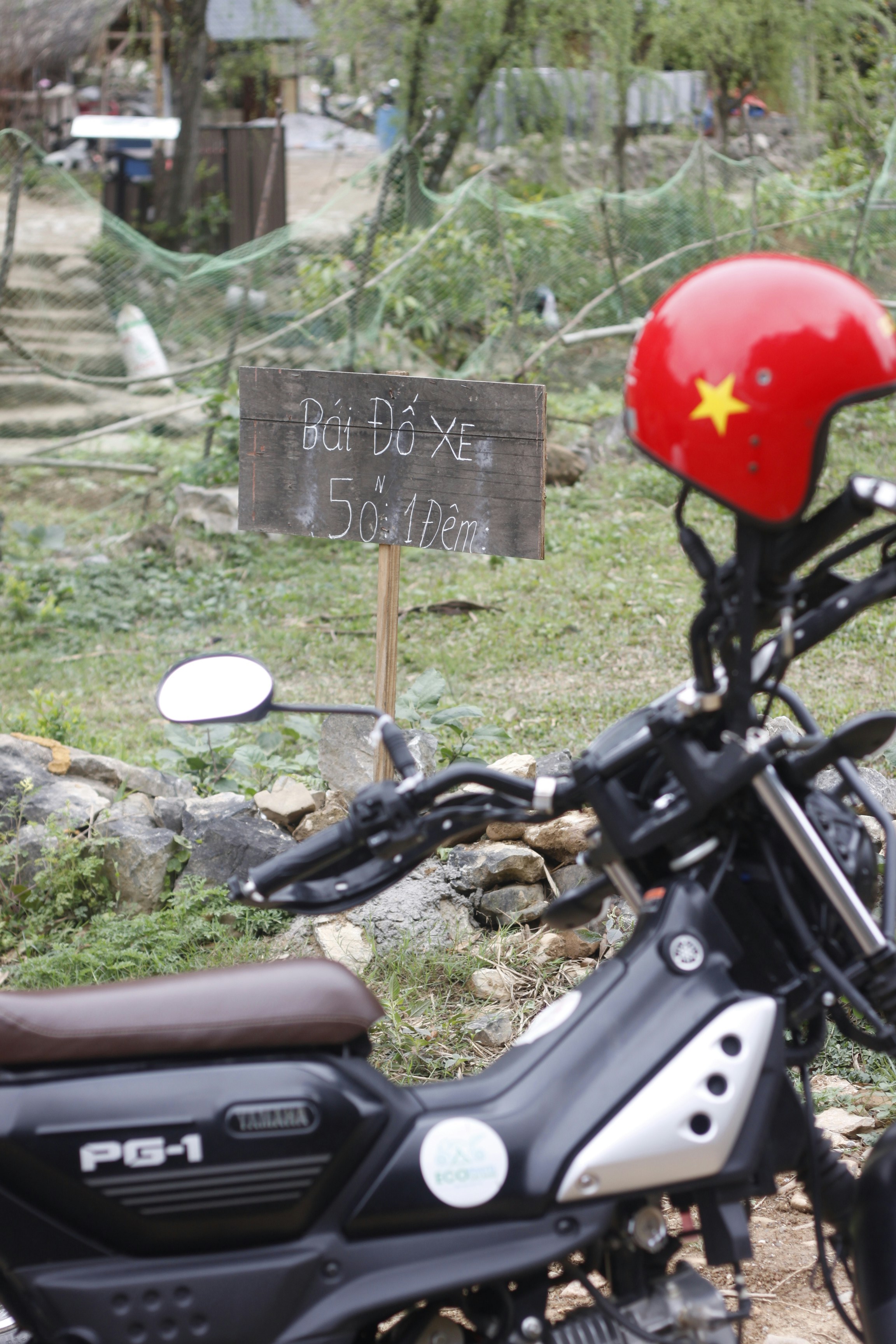 Motorcycle with a red helmet adorned with a yellow star parked near a rustic wooden sign in a rural setting.