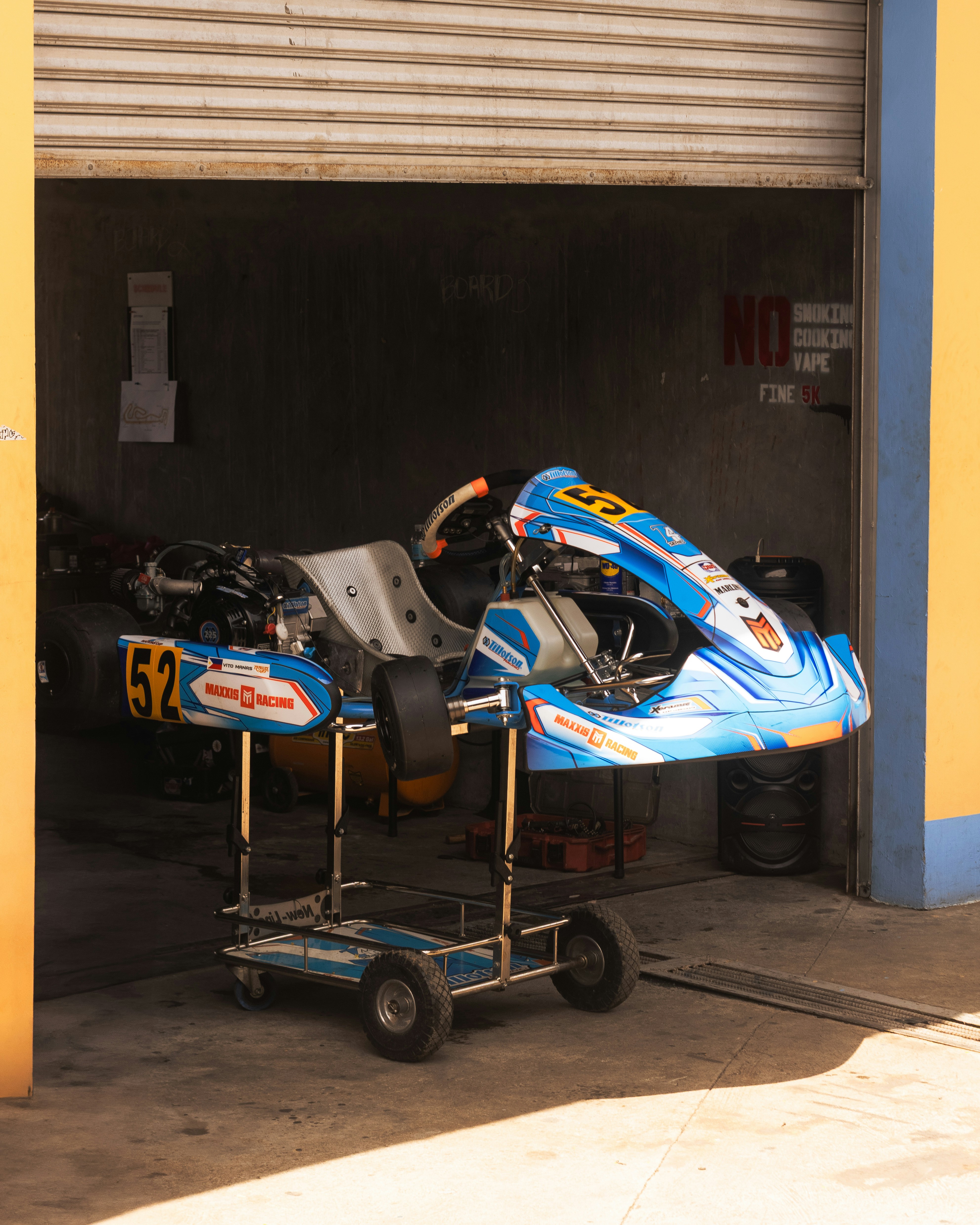 A go-kart on a stand positioned at the entrance of a garage, bathed in sunlight.