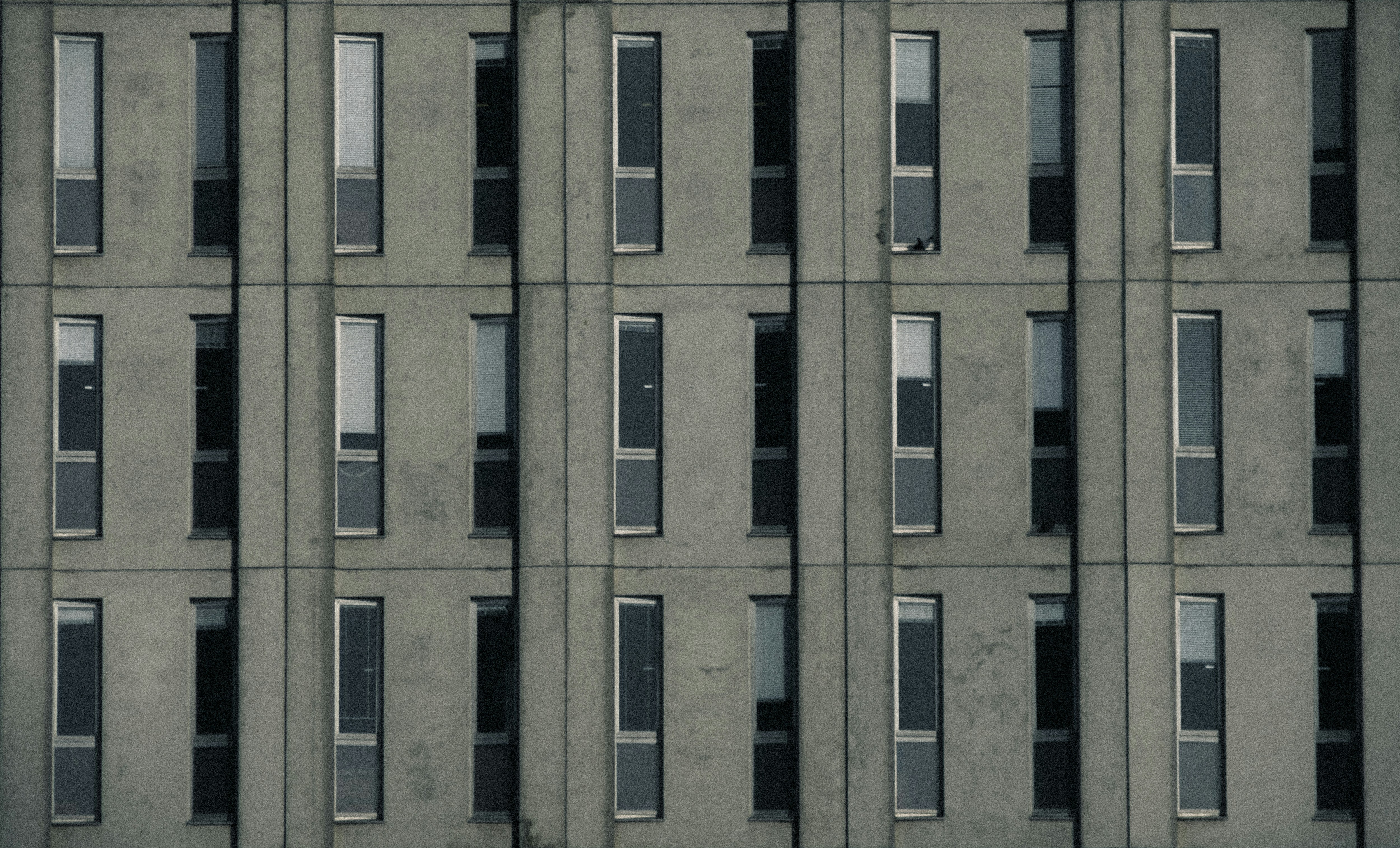 Facade of a modern building showcasing a rhythmic pattern of windows and concrete. The design emphasizes geometric shapes and urban architecture.