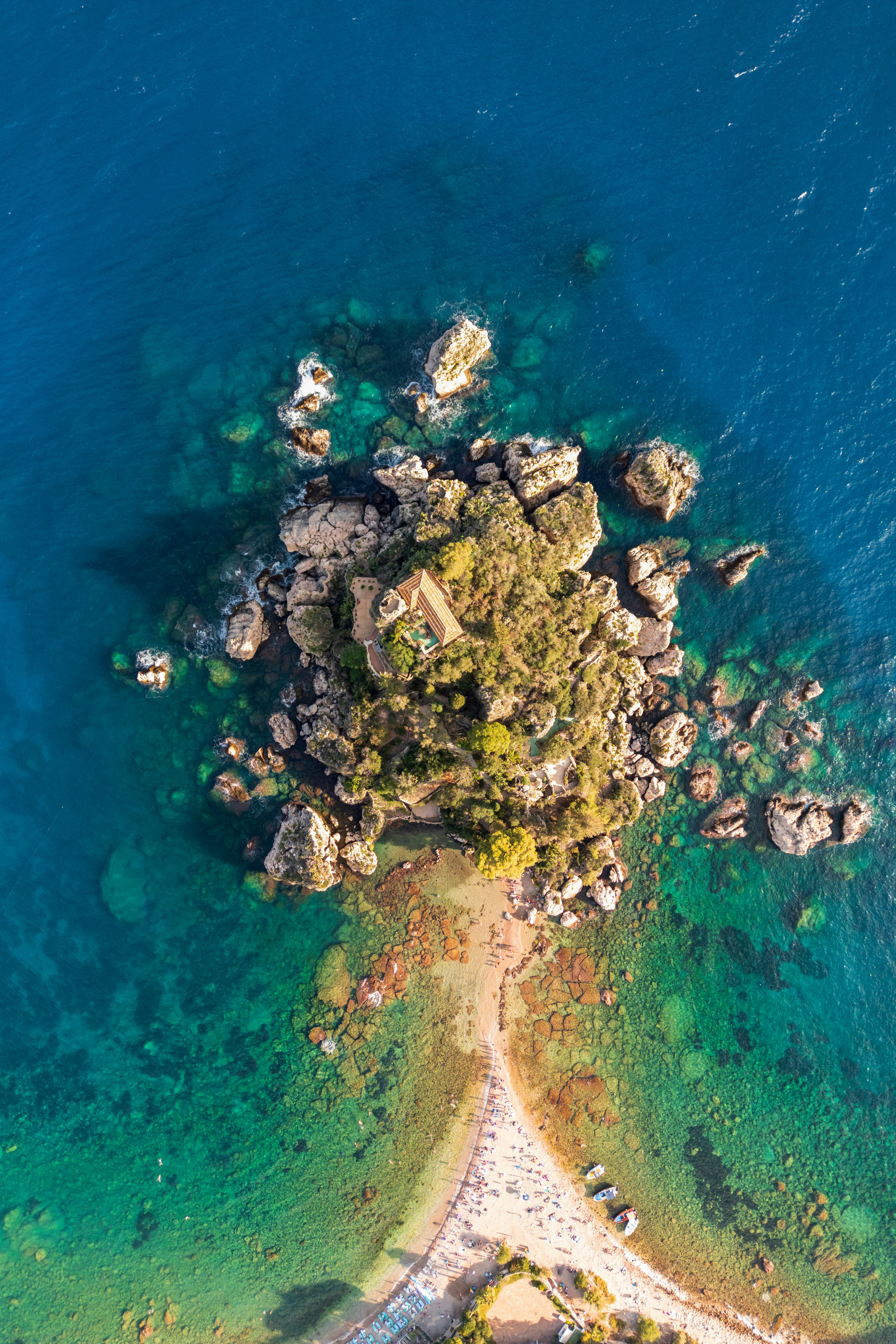 Aerial view of a rocky island with lush greenery surrounded by vibrant blue water.