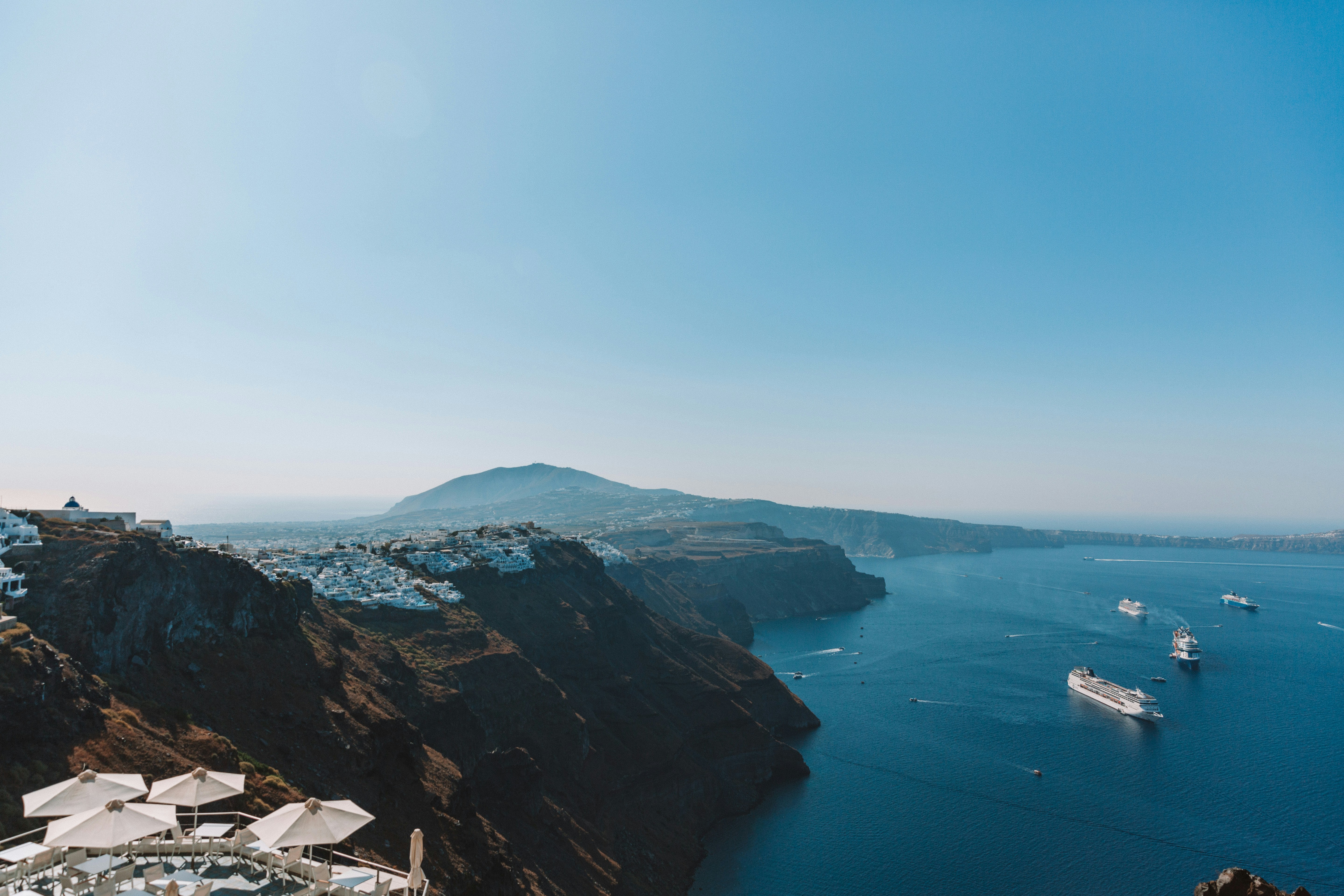 Cruise ships navigate the deep blue waters near a rocky coastline under a clear sky.