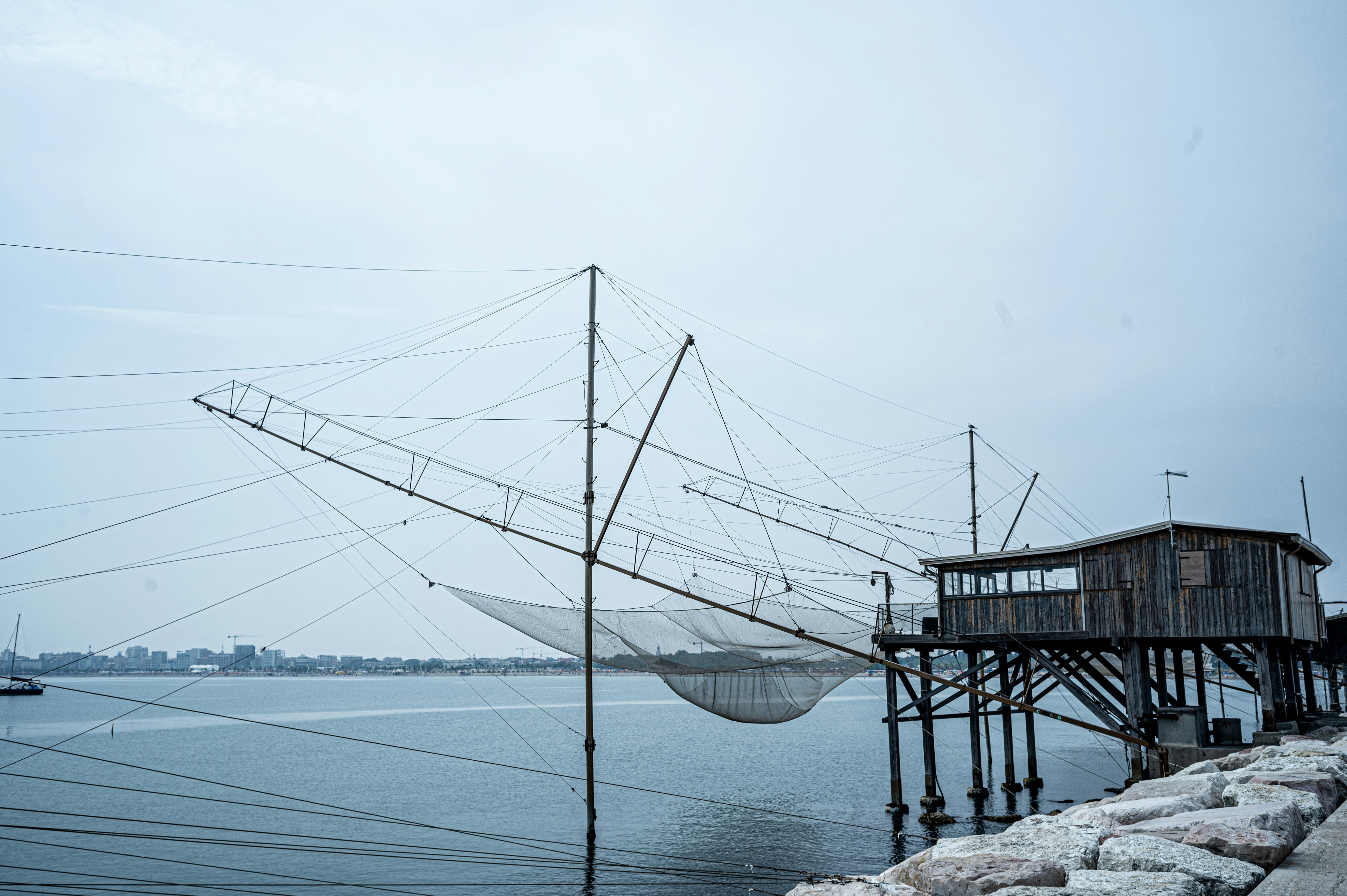 Fishing nets suspended over calm waters near a wooden pier on an overcast day.