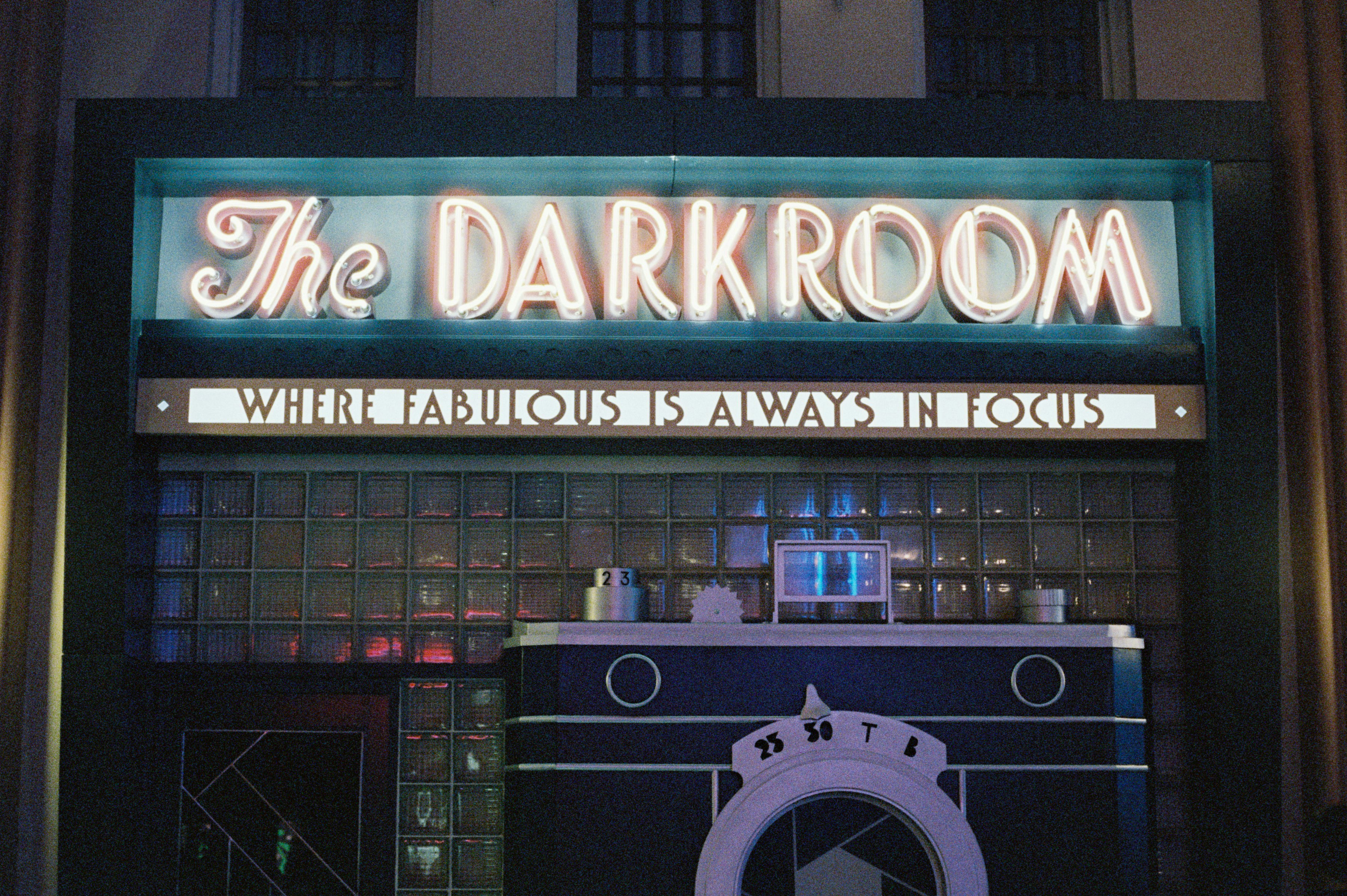 Neon sign of The Darkroom with vintage camera graphic and reflective glass tiles.