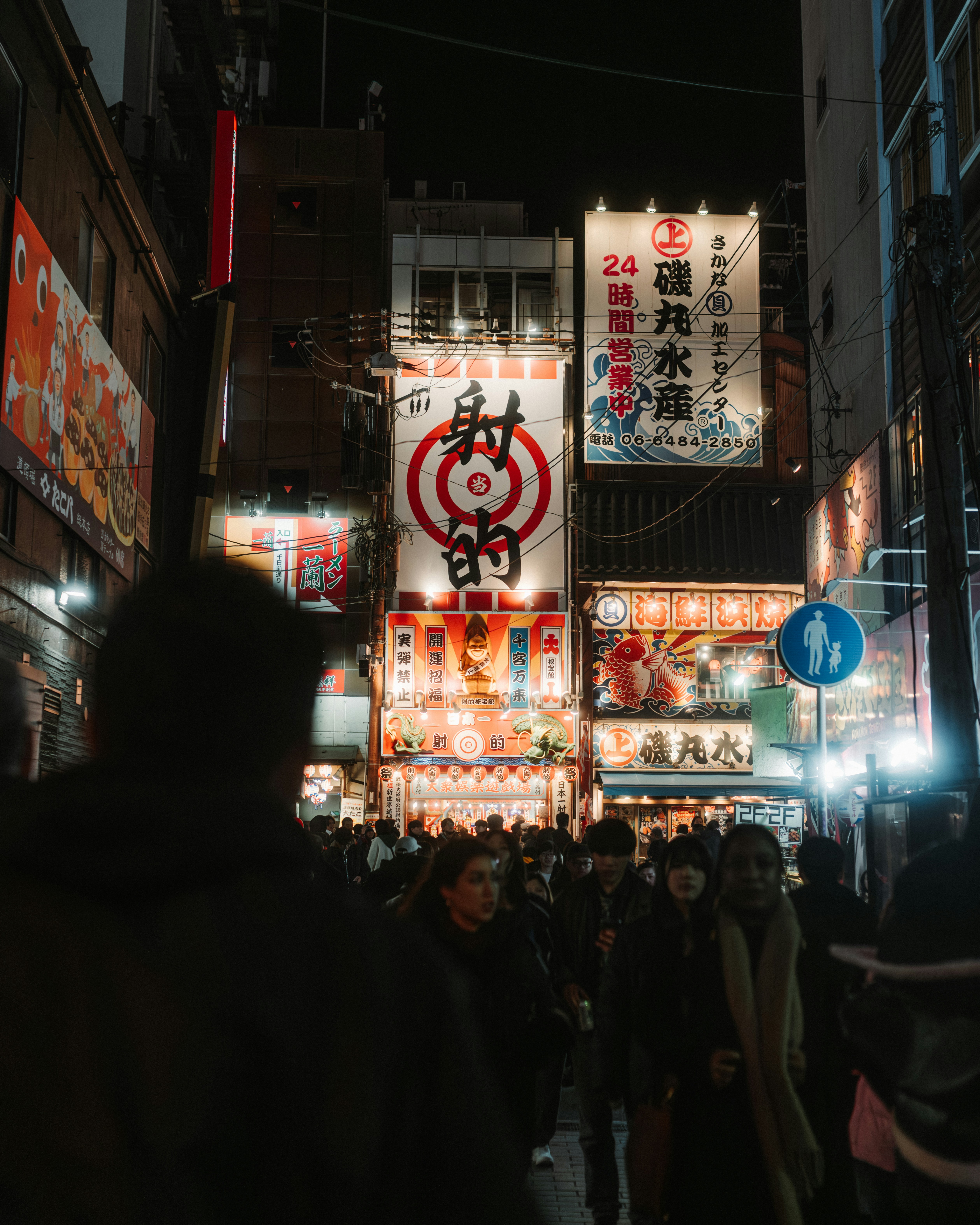 Crowded street in a bustling city at night, illuminated by bright neon signs and colorful banners.