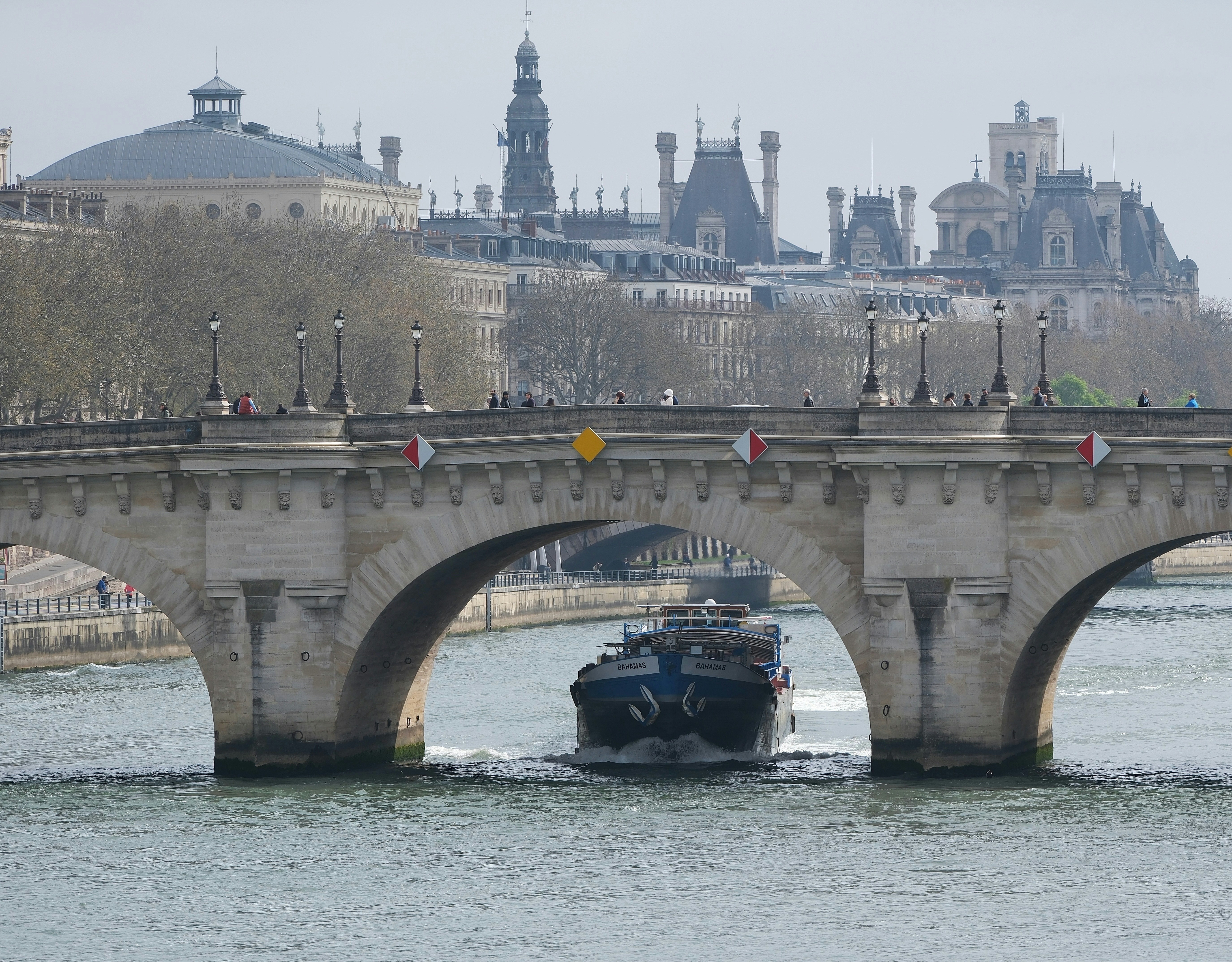 Historic bridge arches over the Seine with a boat passing beneath, framed by Parisian architecture.