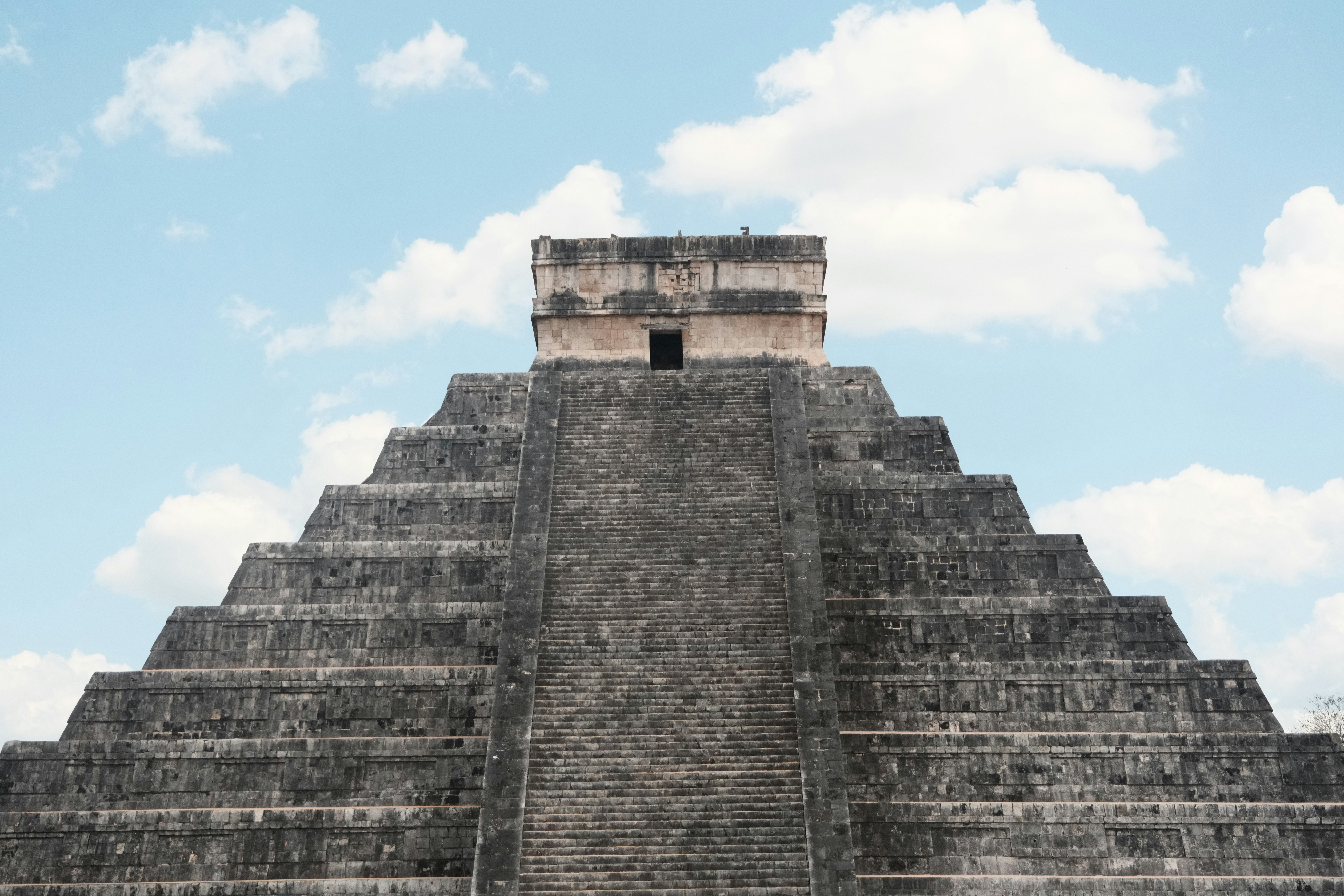 Ancient stone pyramid ascending towards a bright blue sky dotted with fluffy clouds.