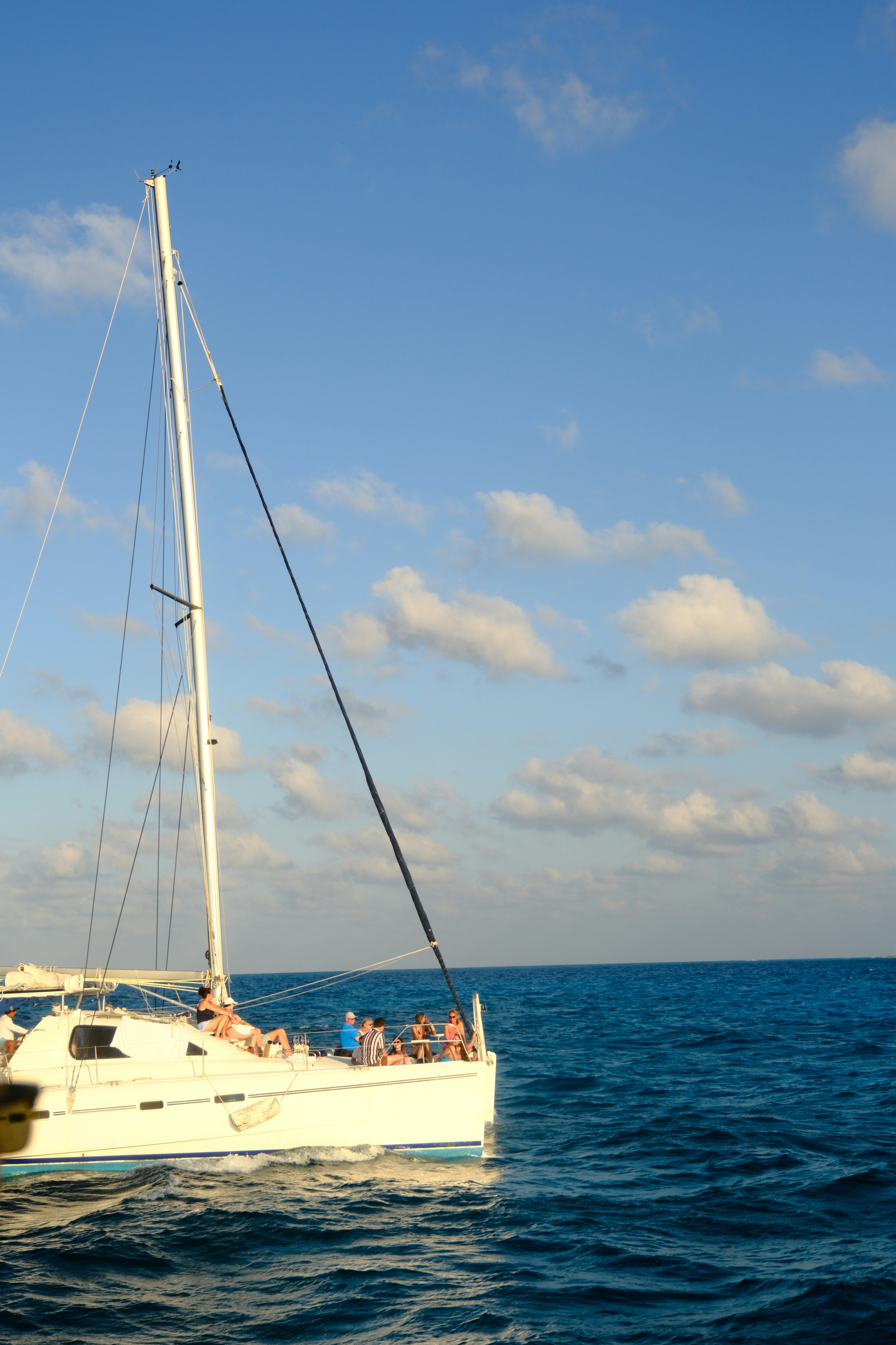 Sailboat gliding on clear blue ocean under a sky dotted with fluffy clouds.