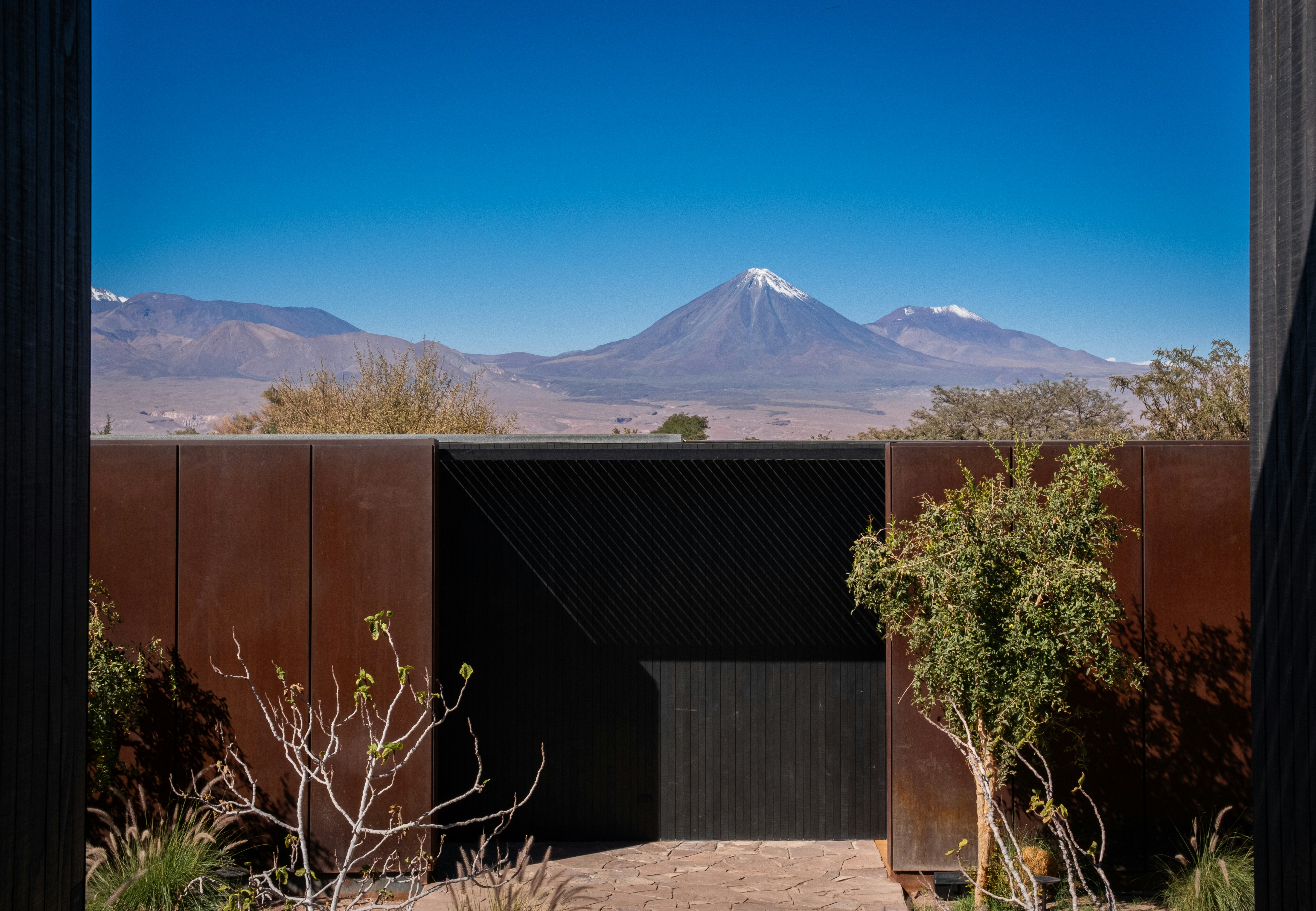 Volcanic landscape framed by modern architecture and desert flora under a clear blue sky.