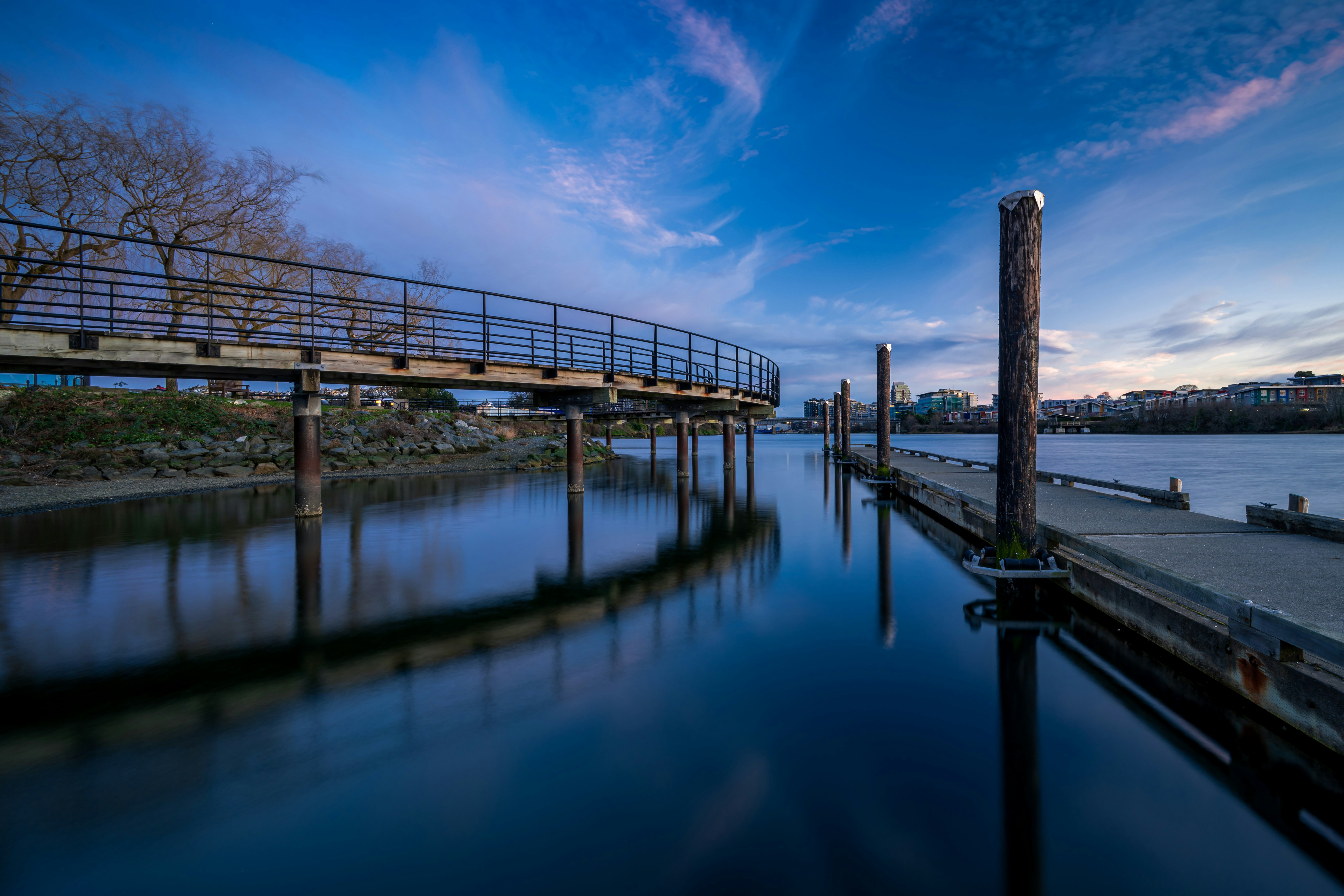 Calm waters under a blue sky with pink clouds, framed by a wooden pier and distant shoreline.