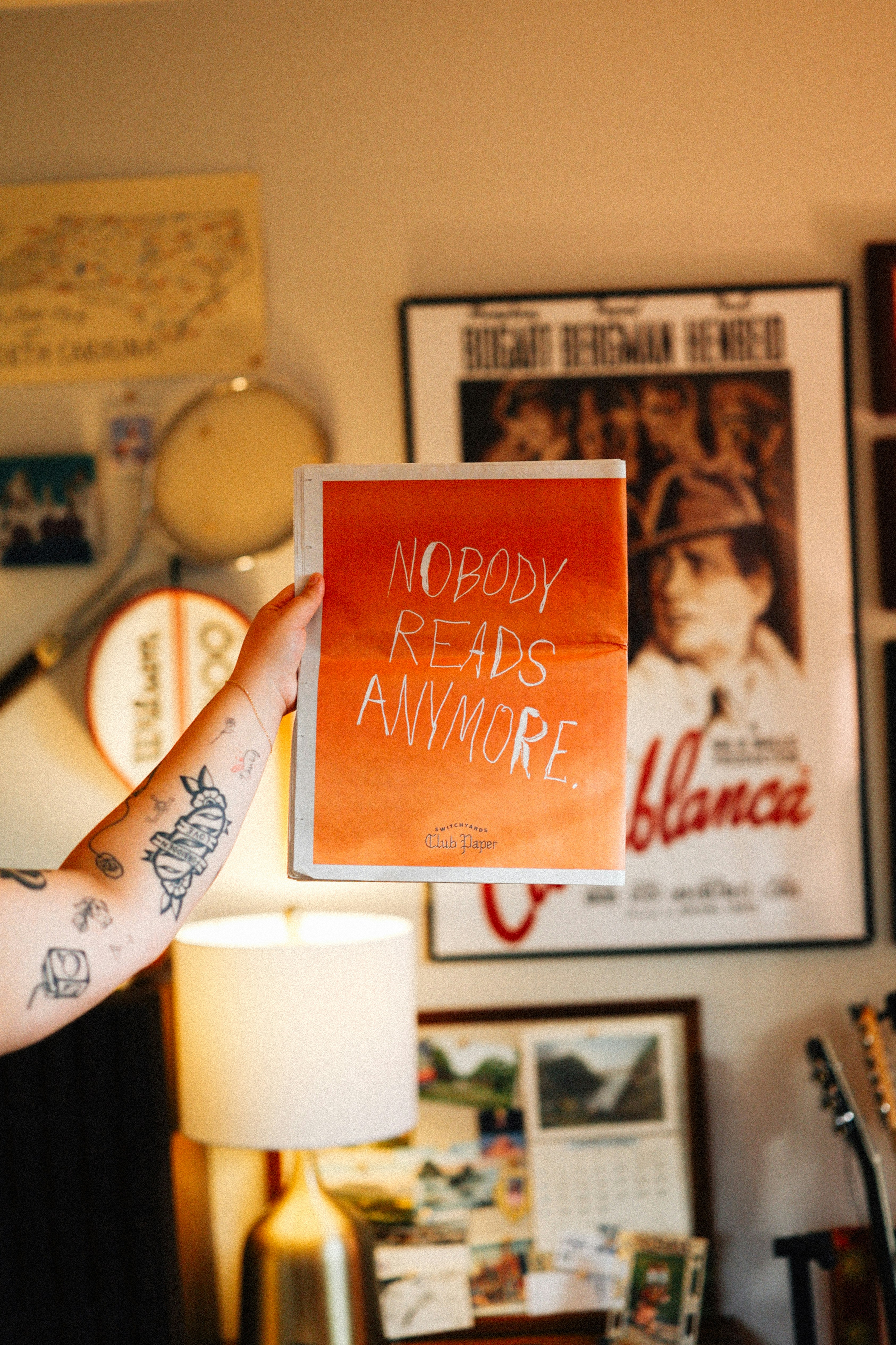 Woman with tattoos holding newspaper that says nobody reads anymore