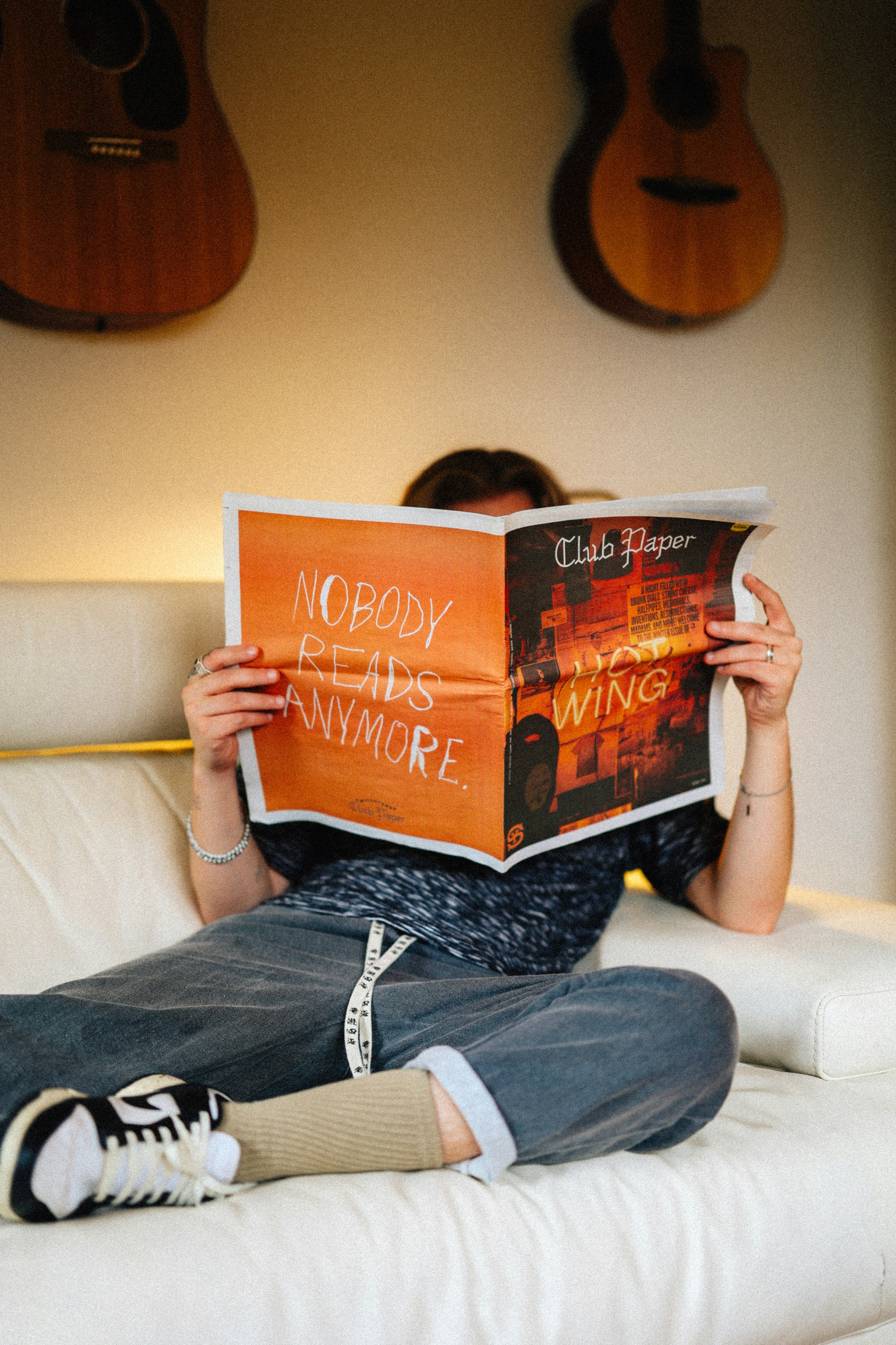 Man reading a newspaper that says "nobody reads anymore" | Person reads a newspaper on a couch.