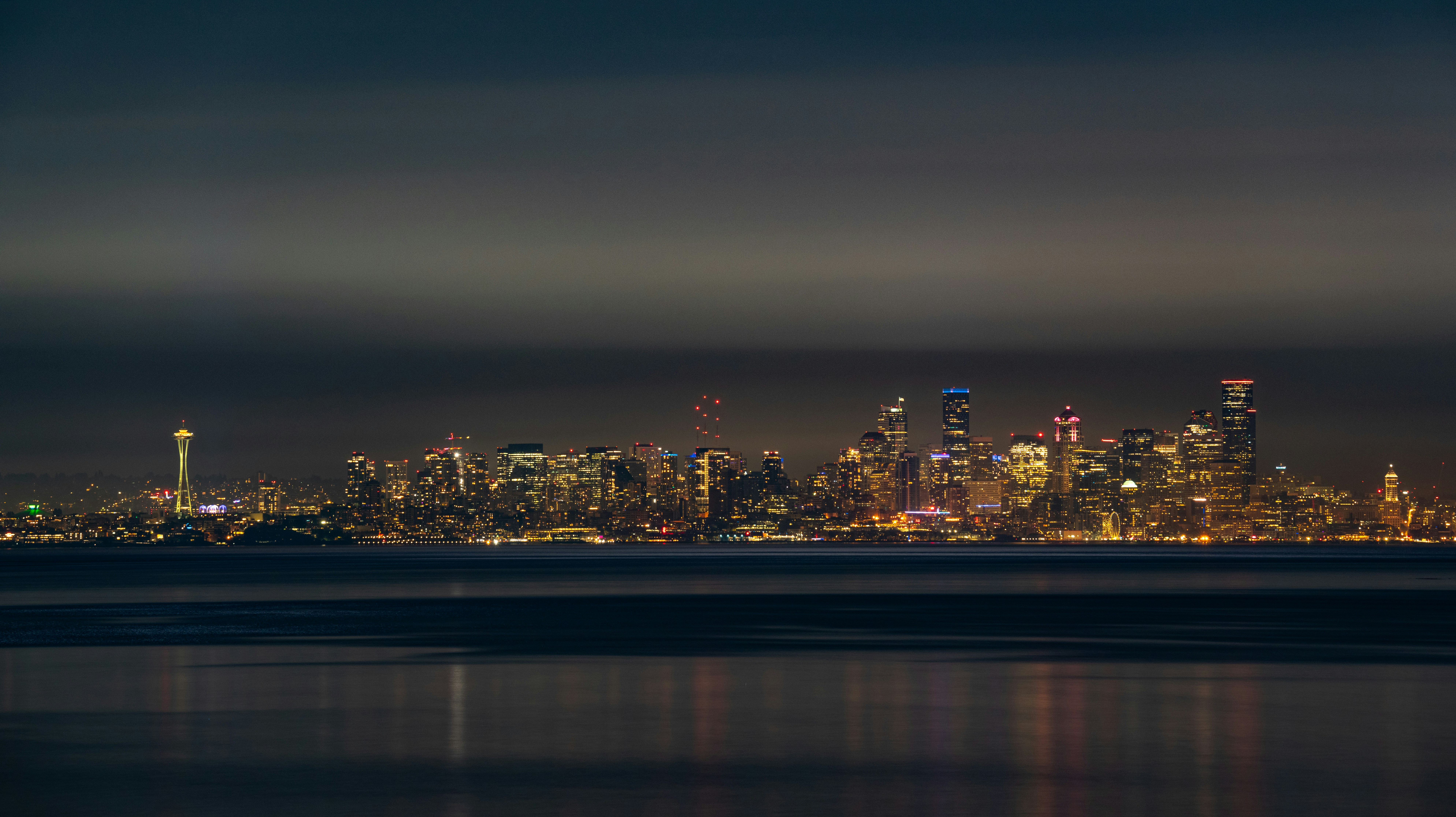 Seattle skyline illuminated against a deep night sky, viewed from across calm water.