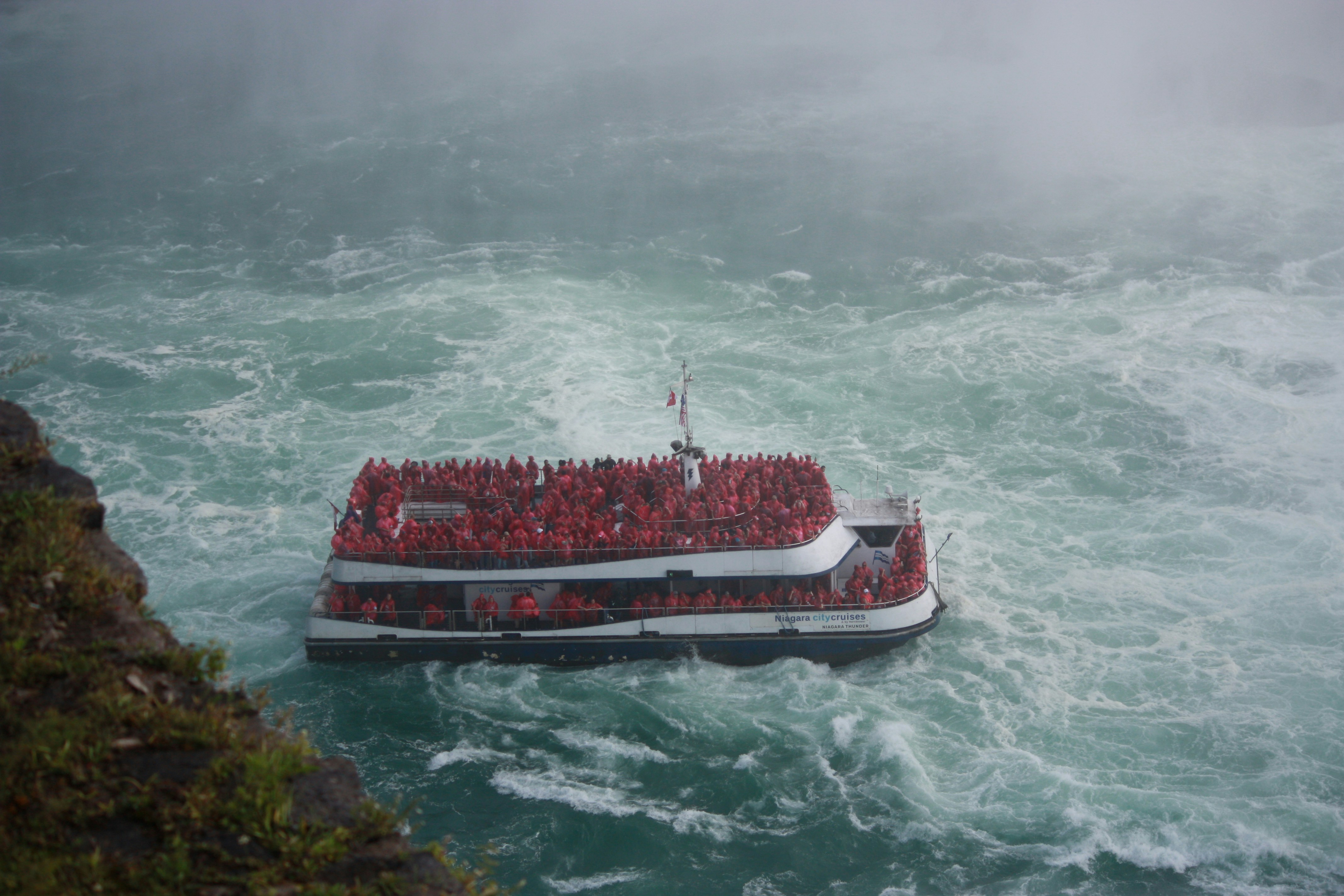 Tour boat navigates churning waters near a misty waterfall.