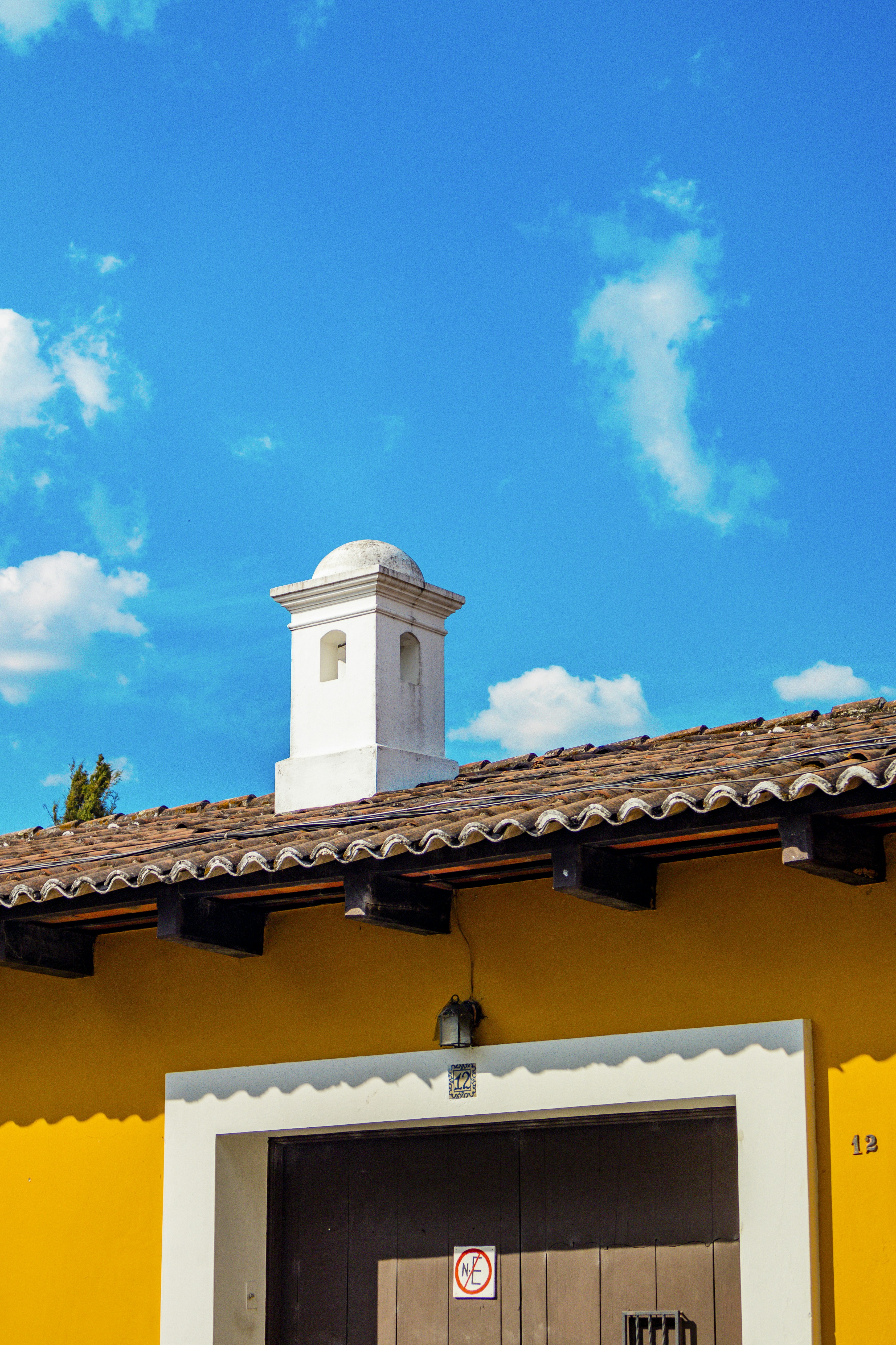 Bright yellow building with a tiled roof and white tower under a vivid blue sky with scattered clouds.