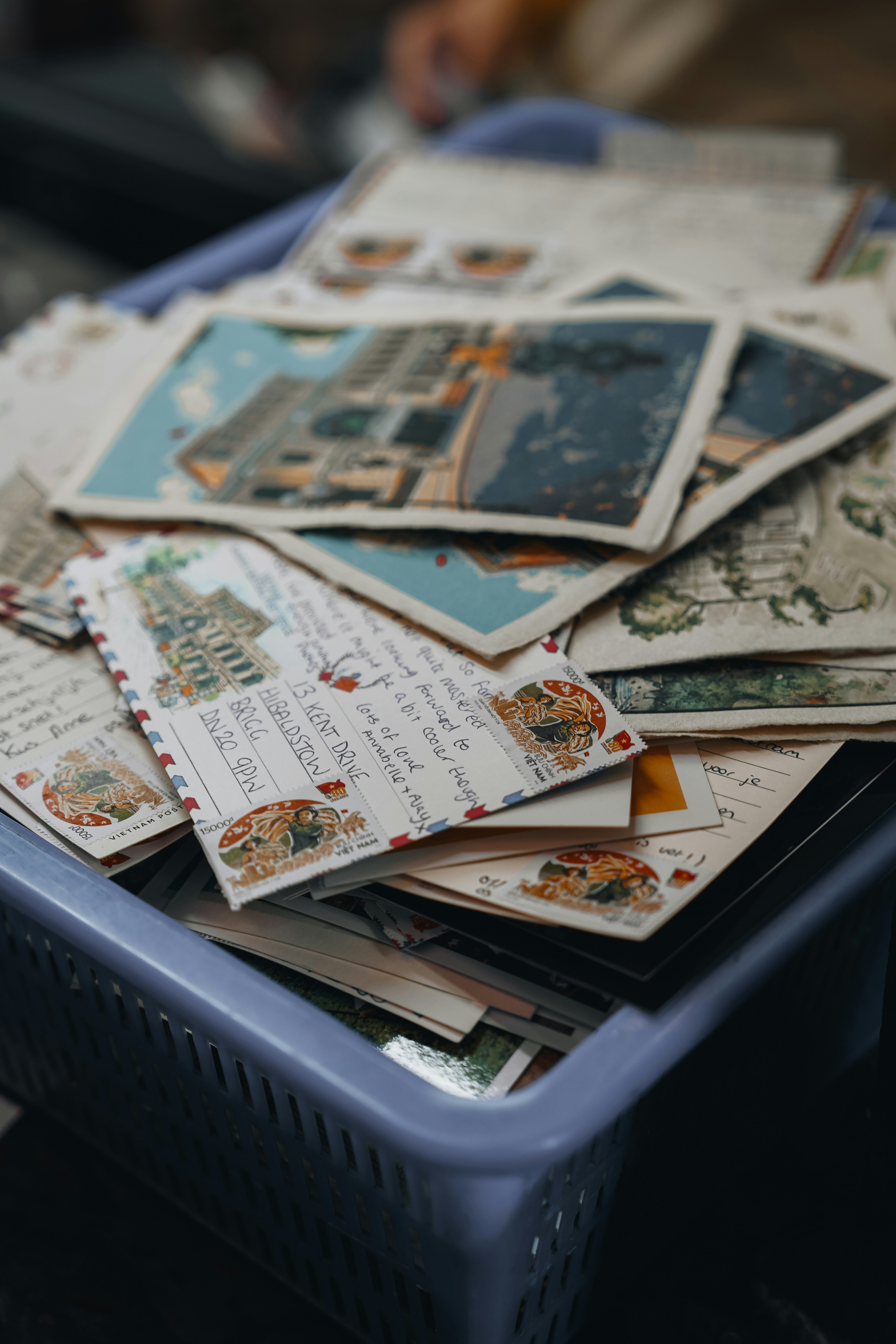 A collection of vintage postcards piled in a blue basket, showcasing various artistic designs and handwritten notes. The scene evokes nostalgia and a sense of history.