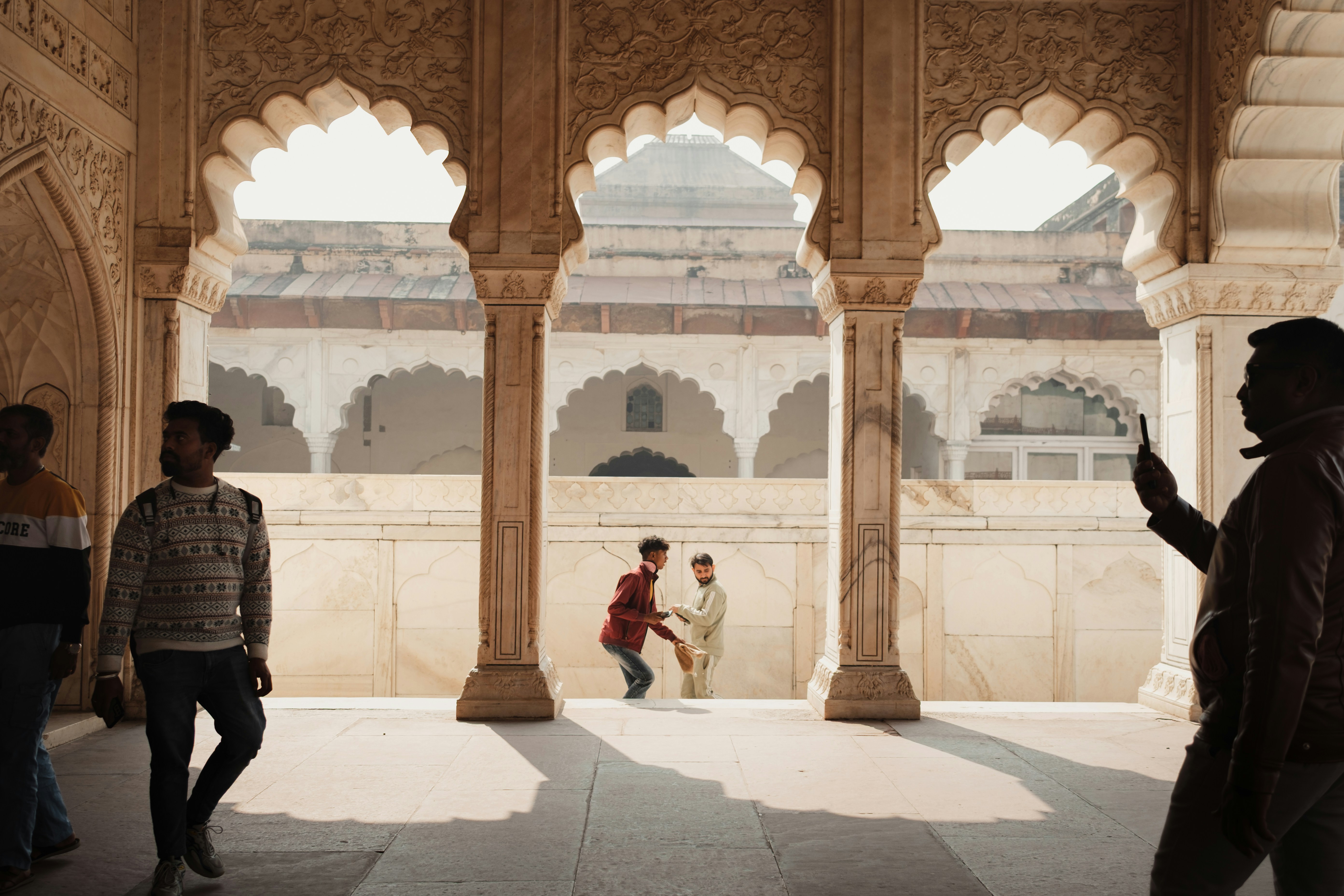 Two Visitors in the Sunlit Mughal Courtyard Framed by Ornate Arches