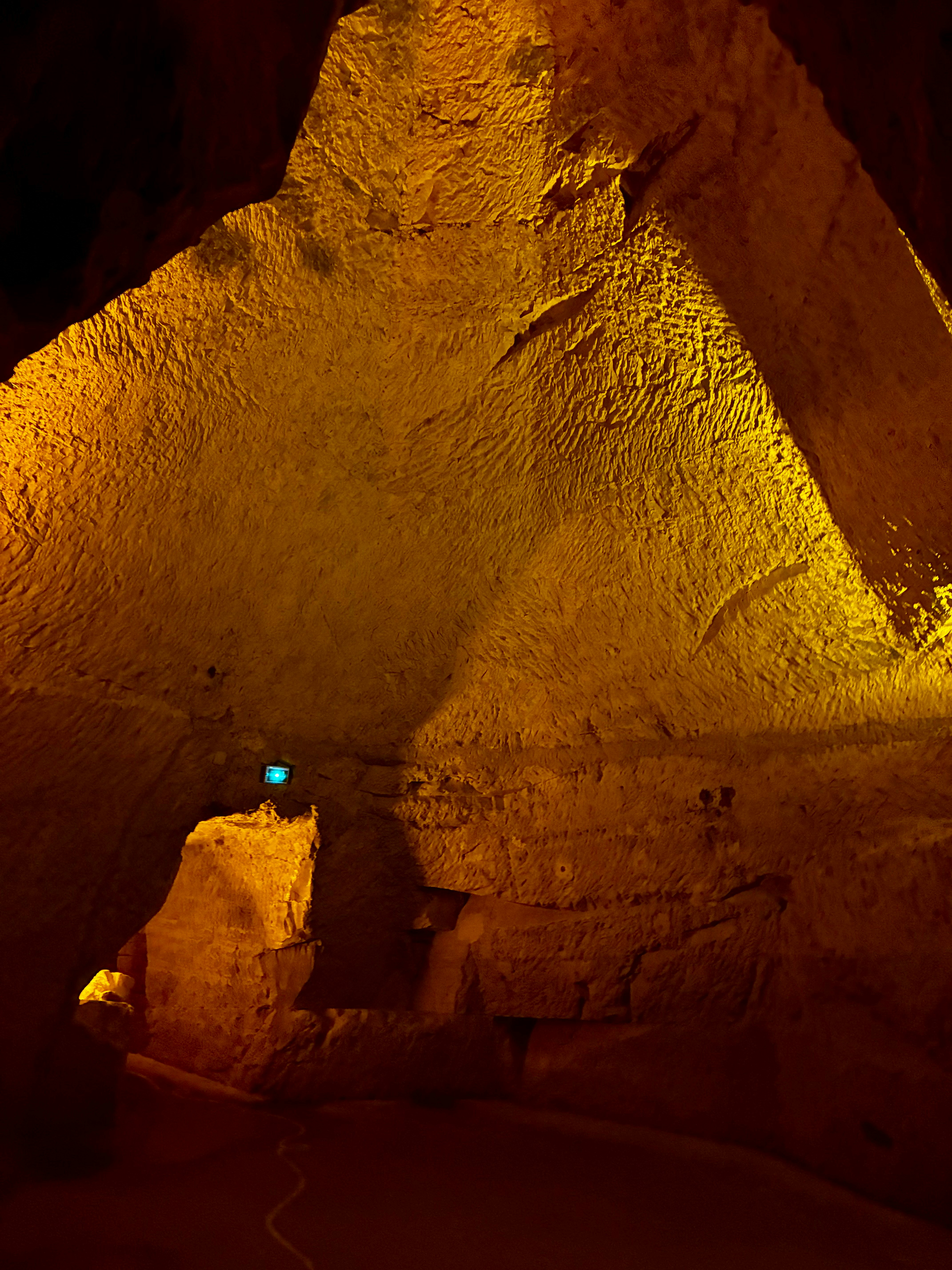 Illuminated cave interior showcasing textured rock formations and warm lighting. A faint blue light hints at the cave's depth.