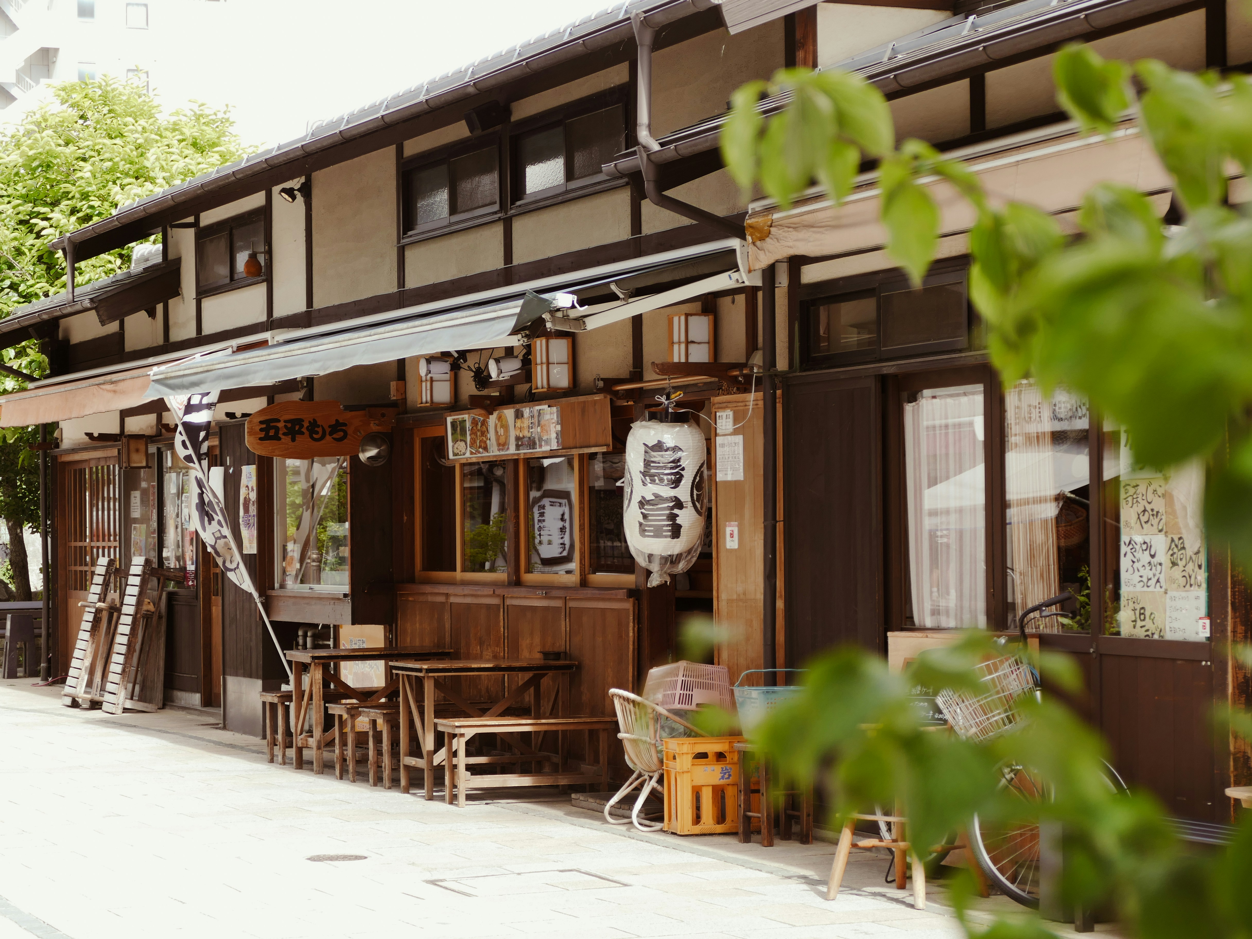 Traditional wooden Japanese buildings line a quiet street under a bright sky.