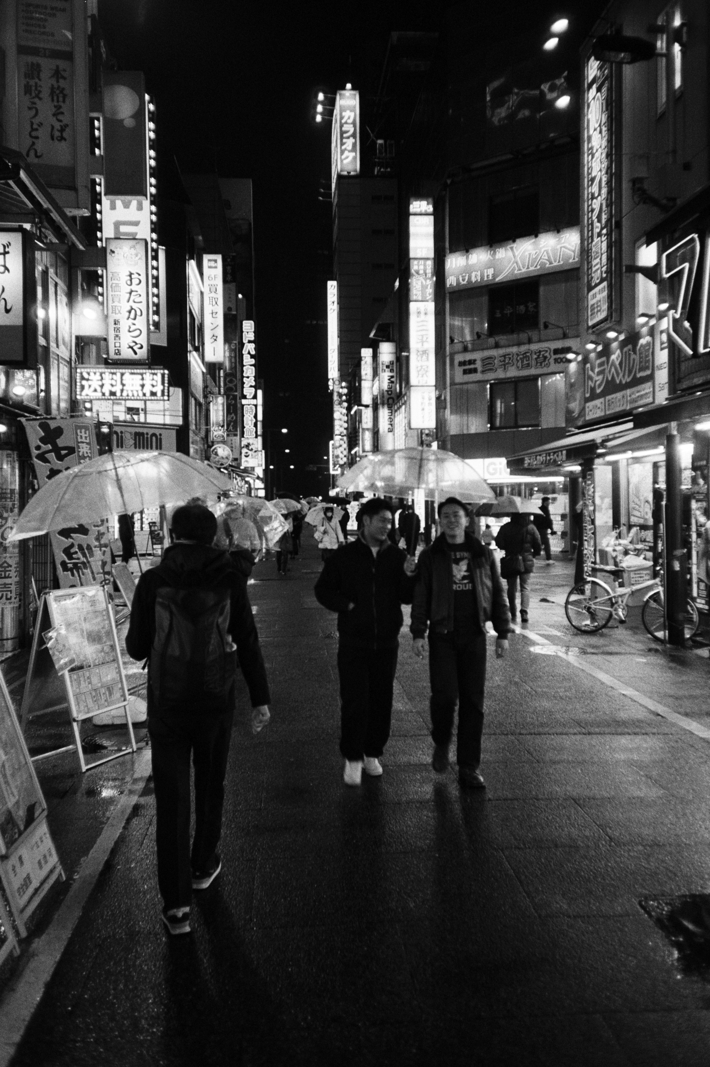 Monochrome city street scene with pedestrians and illuminated signs at night.