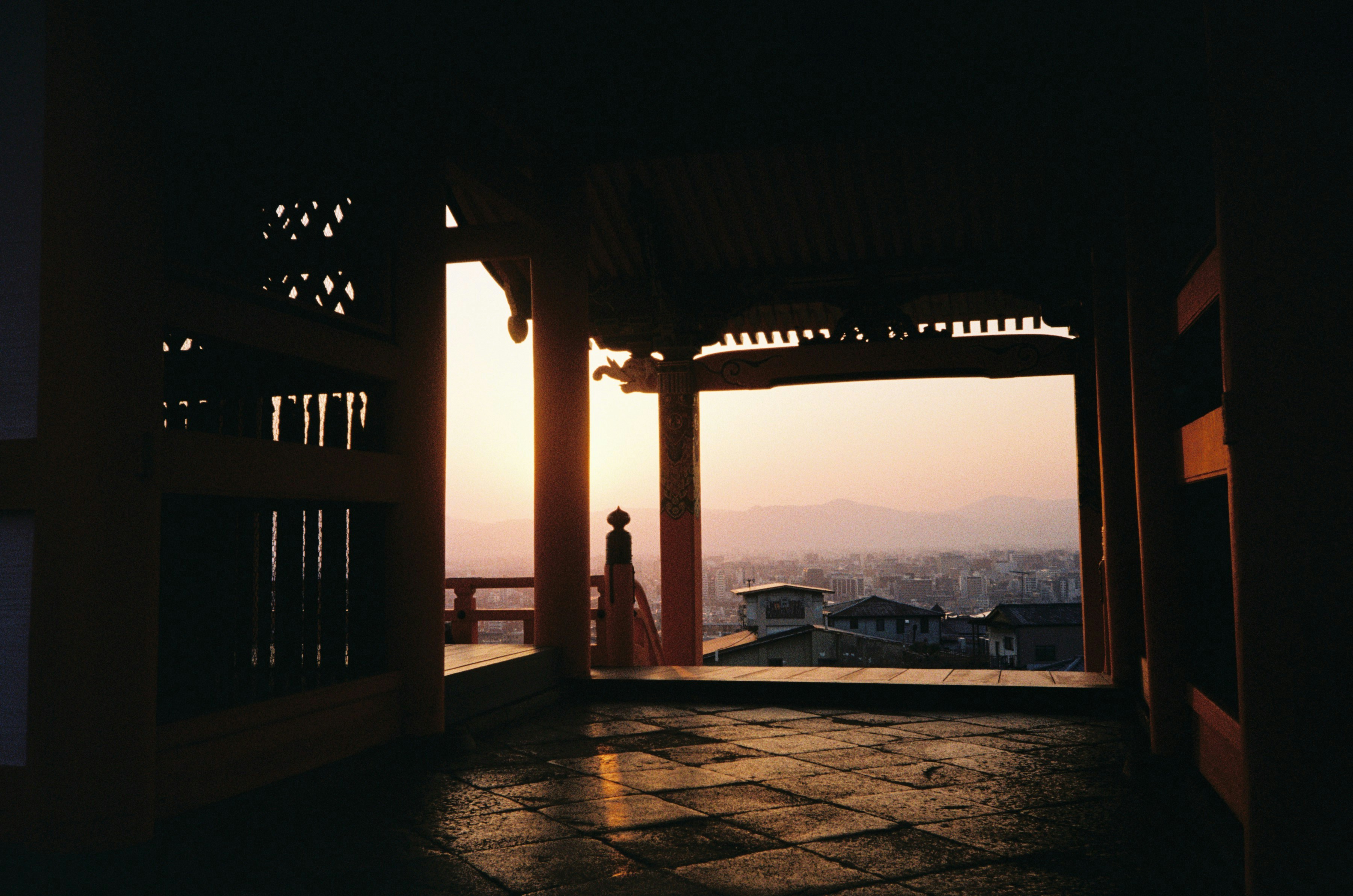 Sunset Threshold: A lone silhouette framed by a temple balcony overlooking a sunlit city