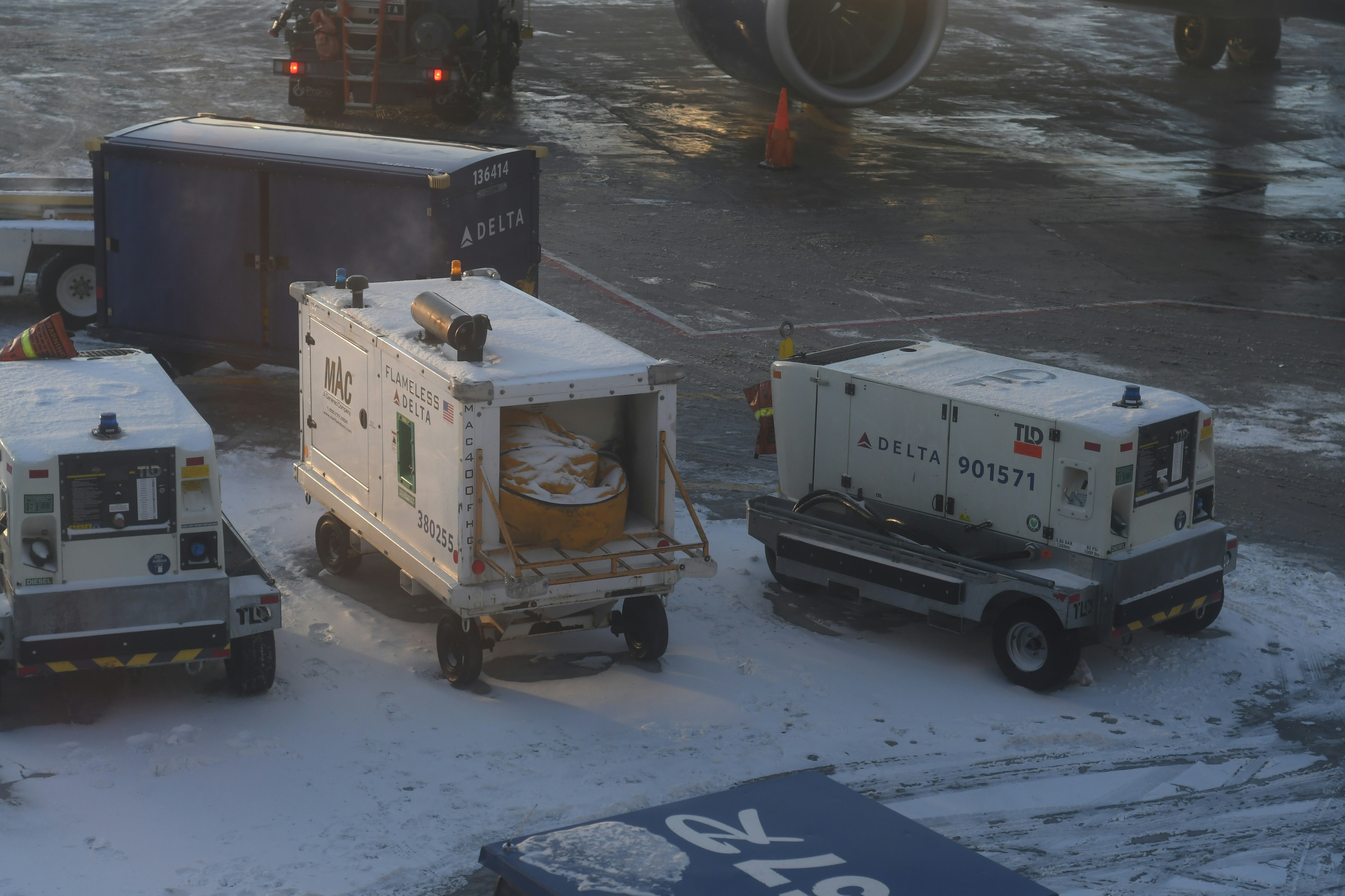 Airport support vehicles are staged on the snowy tarmac.