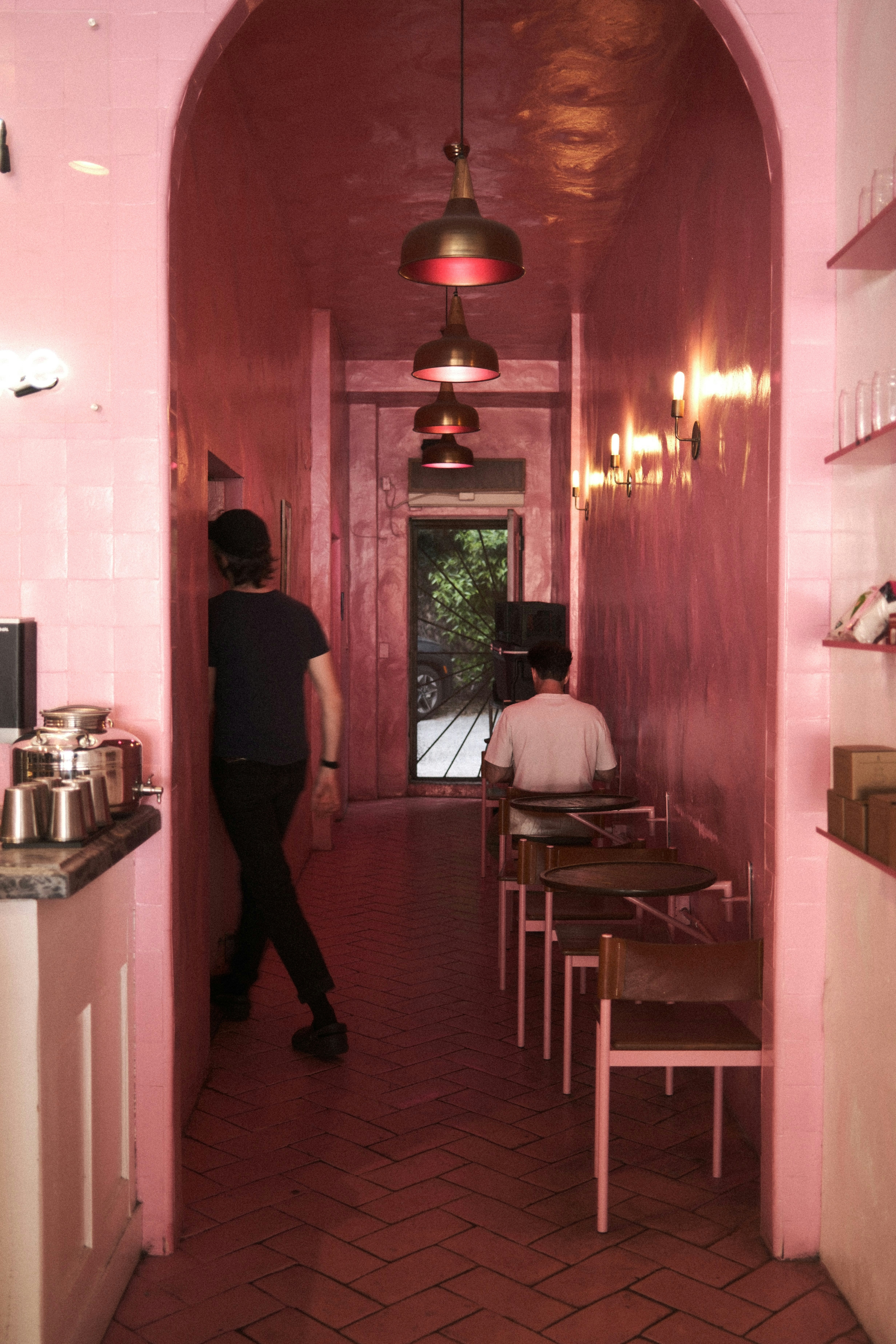 Narrow pink corridor with arched ceiling, featuring a person walking and another seated at a table.