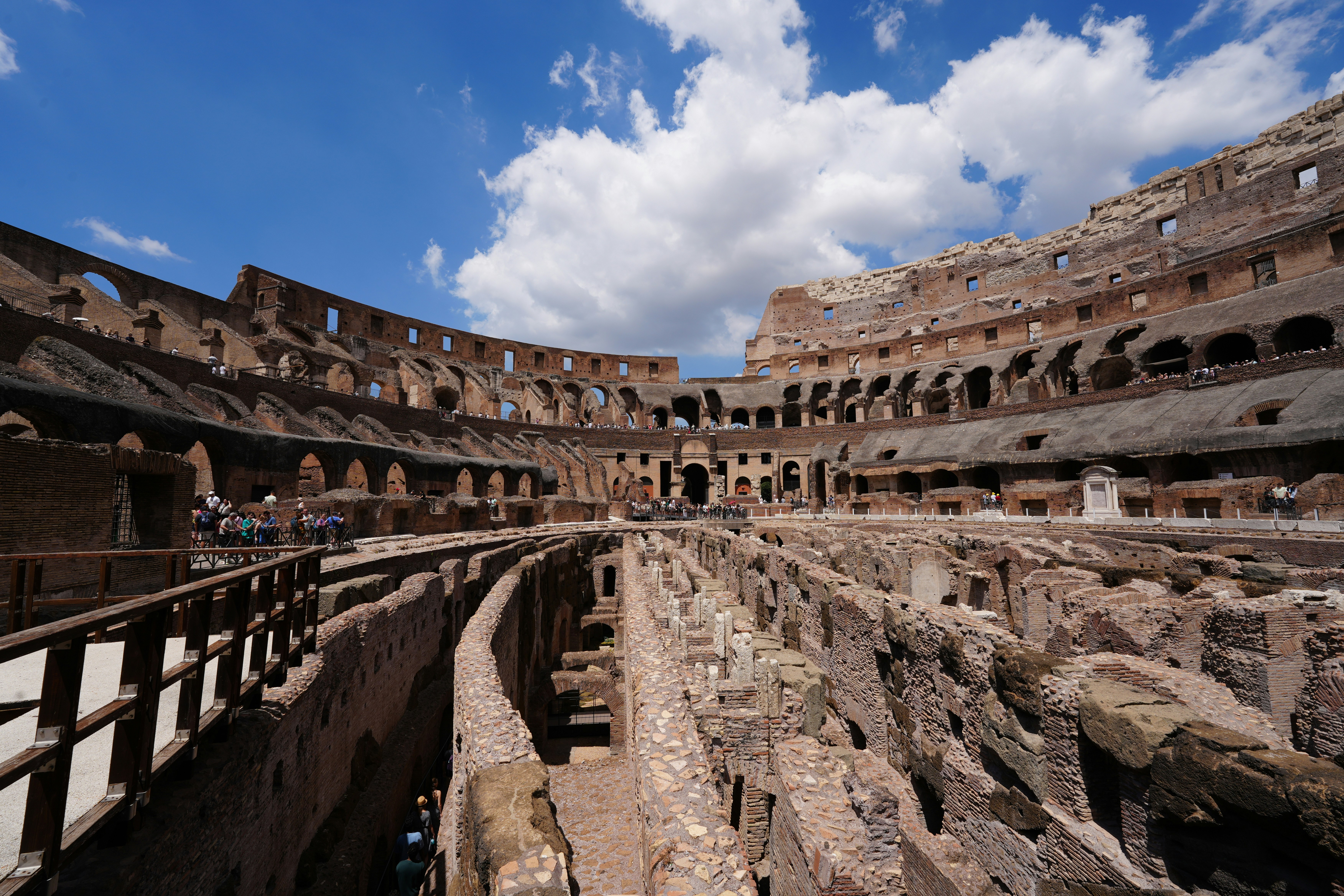 Interior view of the Colosseum with clear blue sky and white clouds overhead.