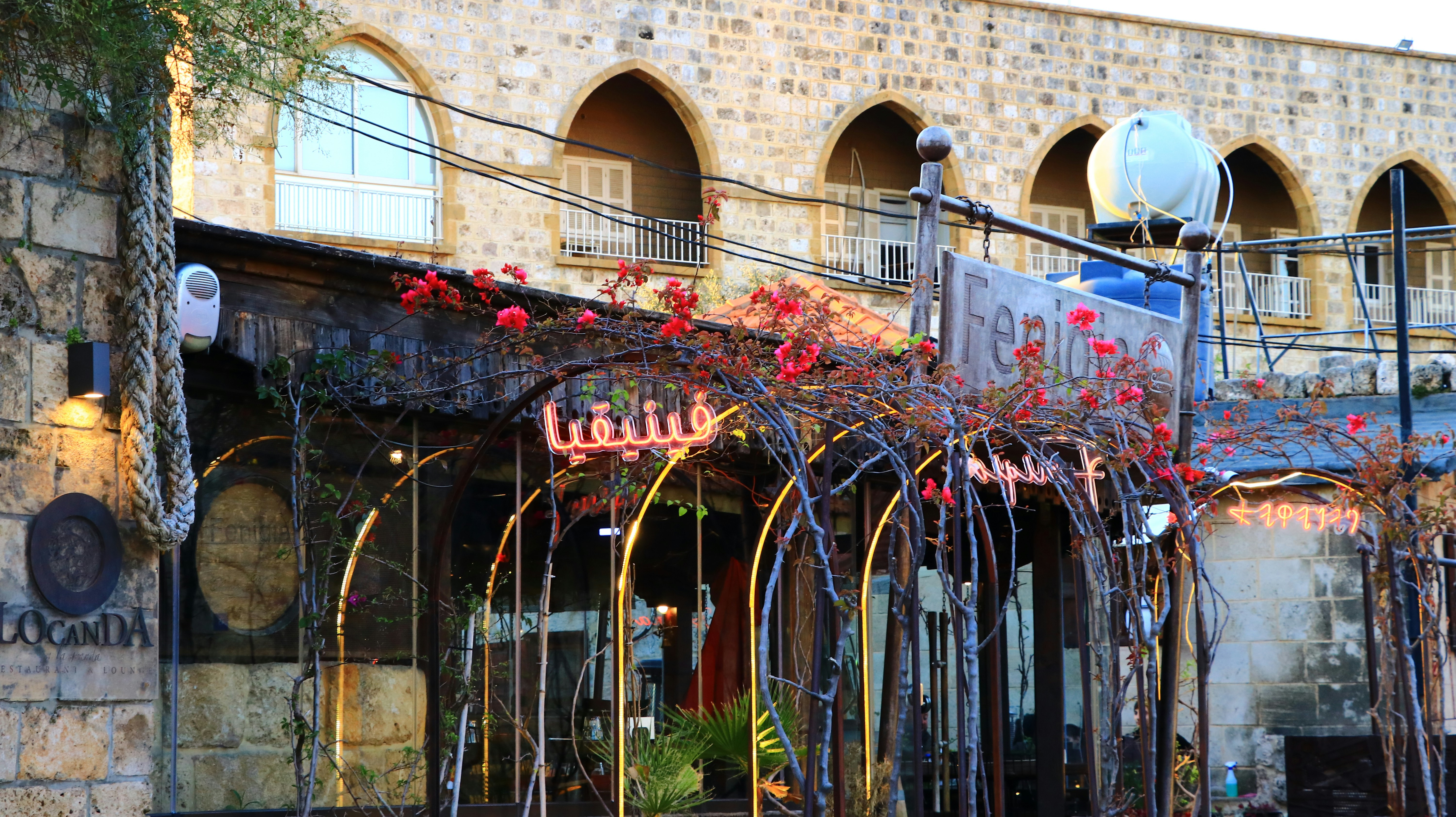 Historic stone building with arched windows and vibrant vines in Byblos under a clear sky.
