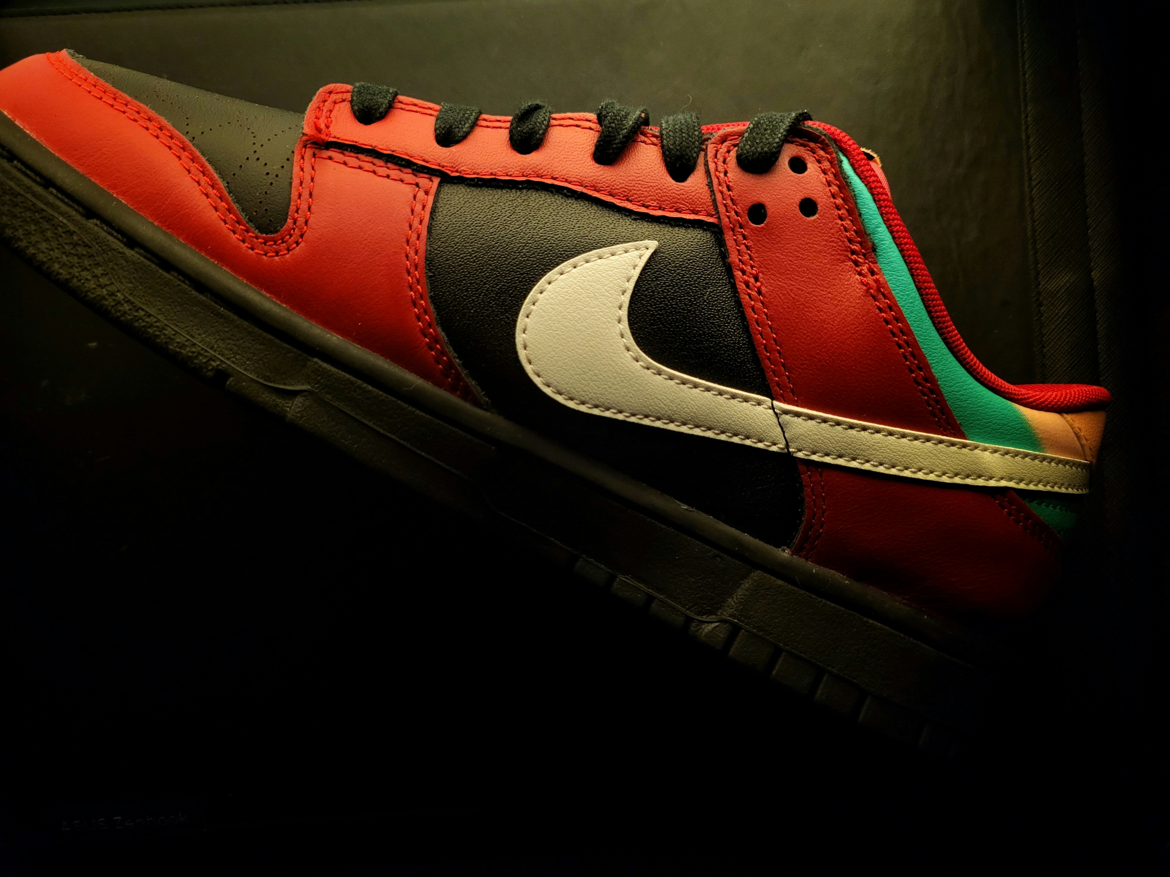 Diagonal red-black sneaker with a white swoosh and teal heel in moody lighting