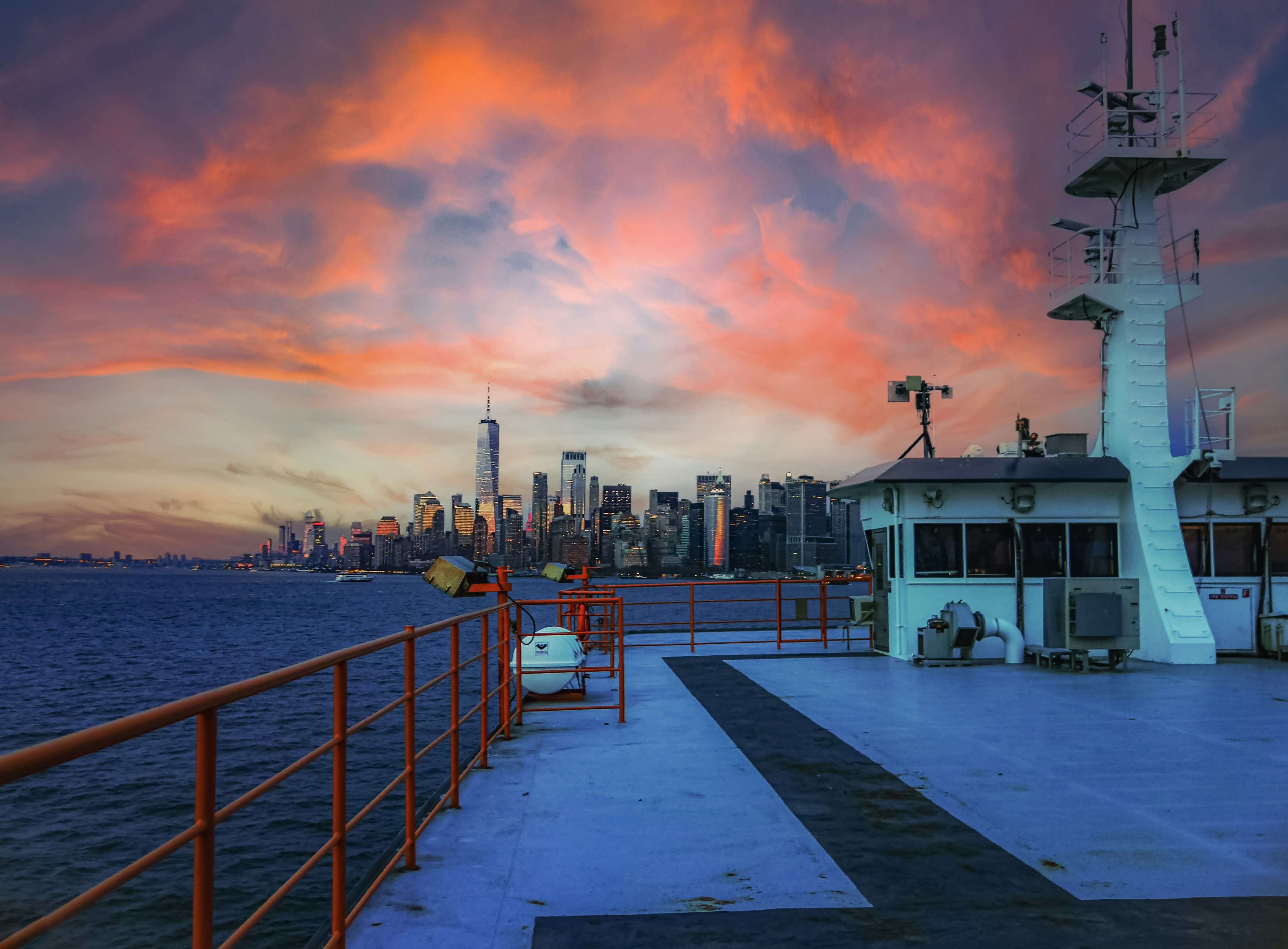 Ferry deck with vibrant sunset sky framing a distant city skyline.