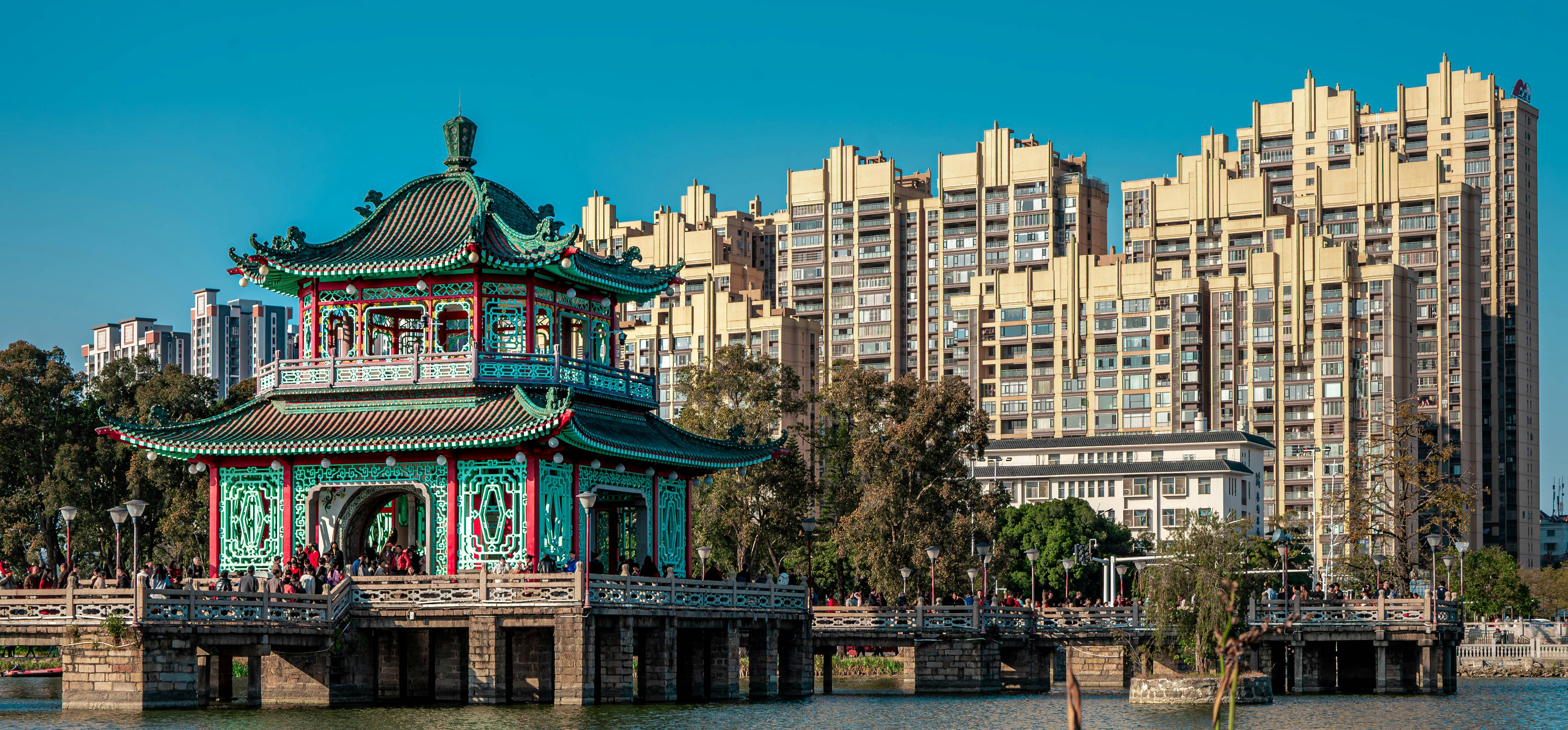Traditional Chinese pavilion set against a backdrop of modern high-rise buildings by a calm lake.