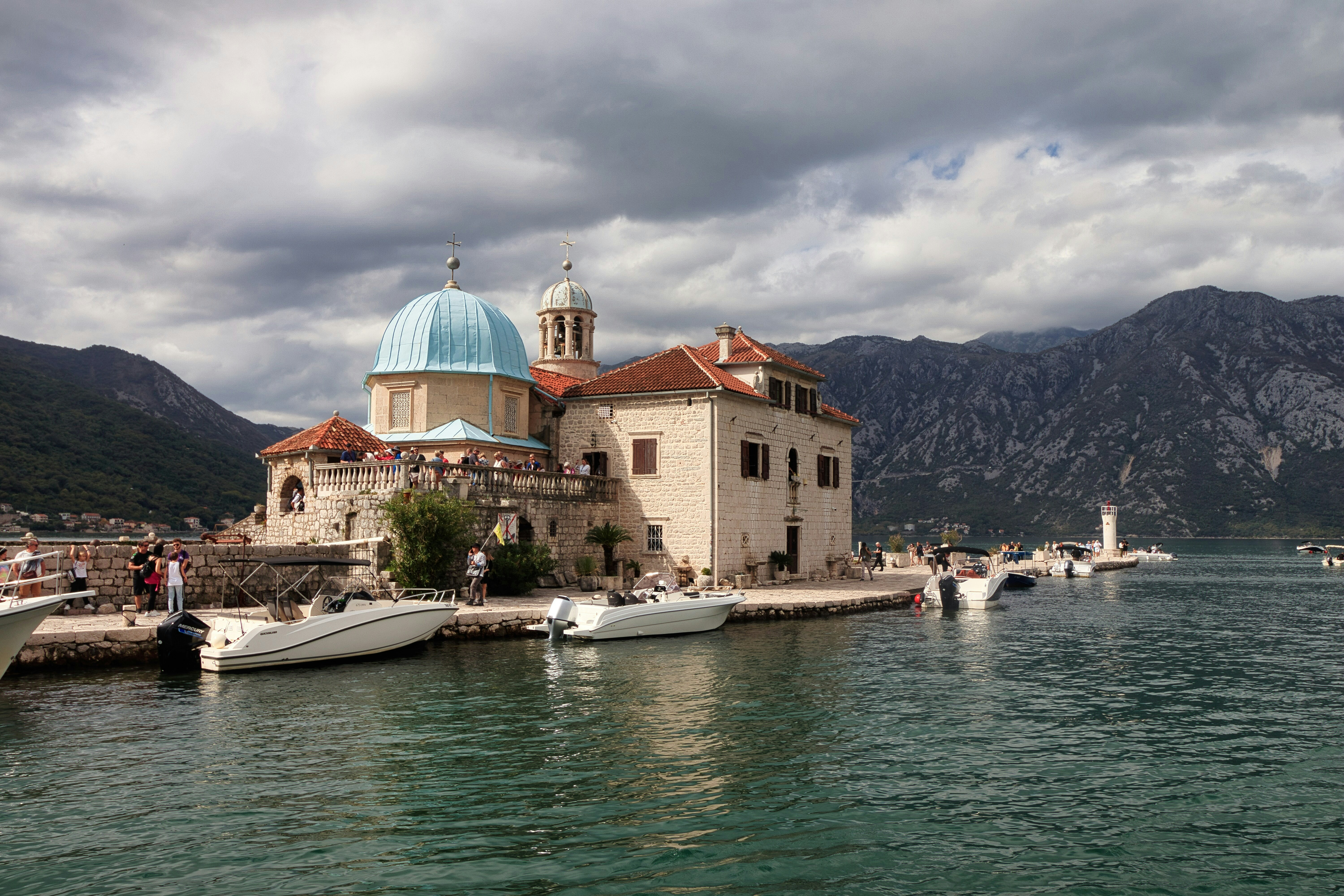 Historic church with a blue dome situated on a small island in the Bay of Kotor under a cloudy sky.
