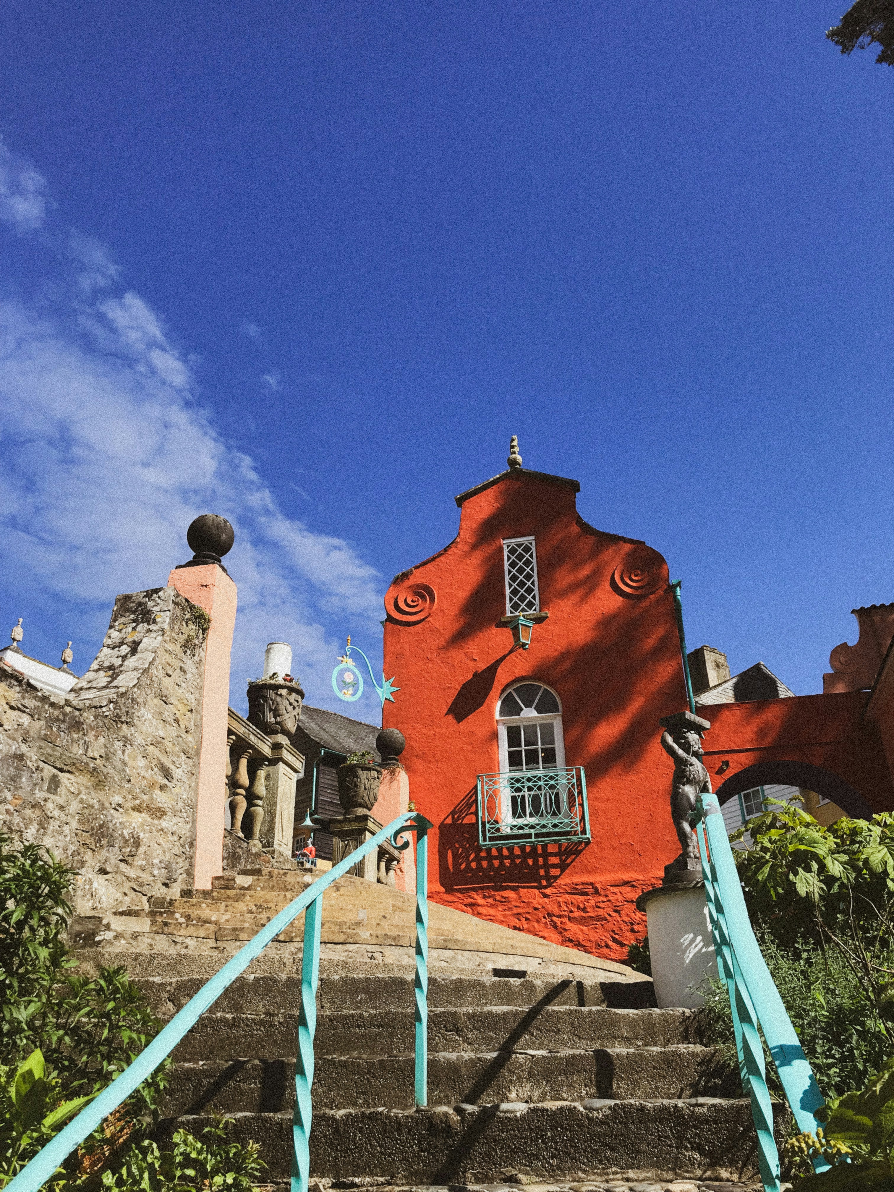 Red building with ornate architecture at the top of stone steps under a bright blue sky.