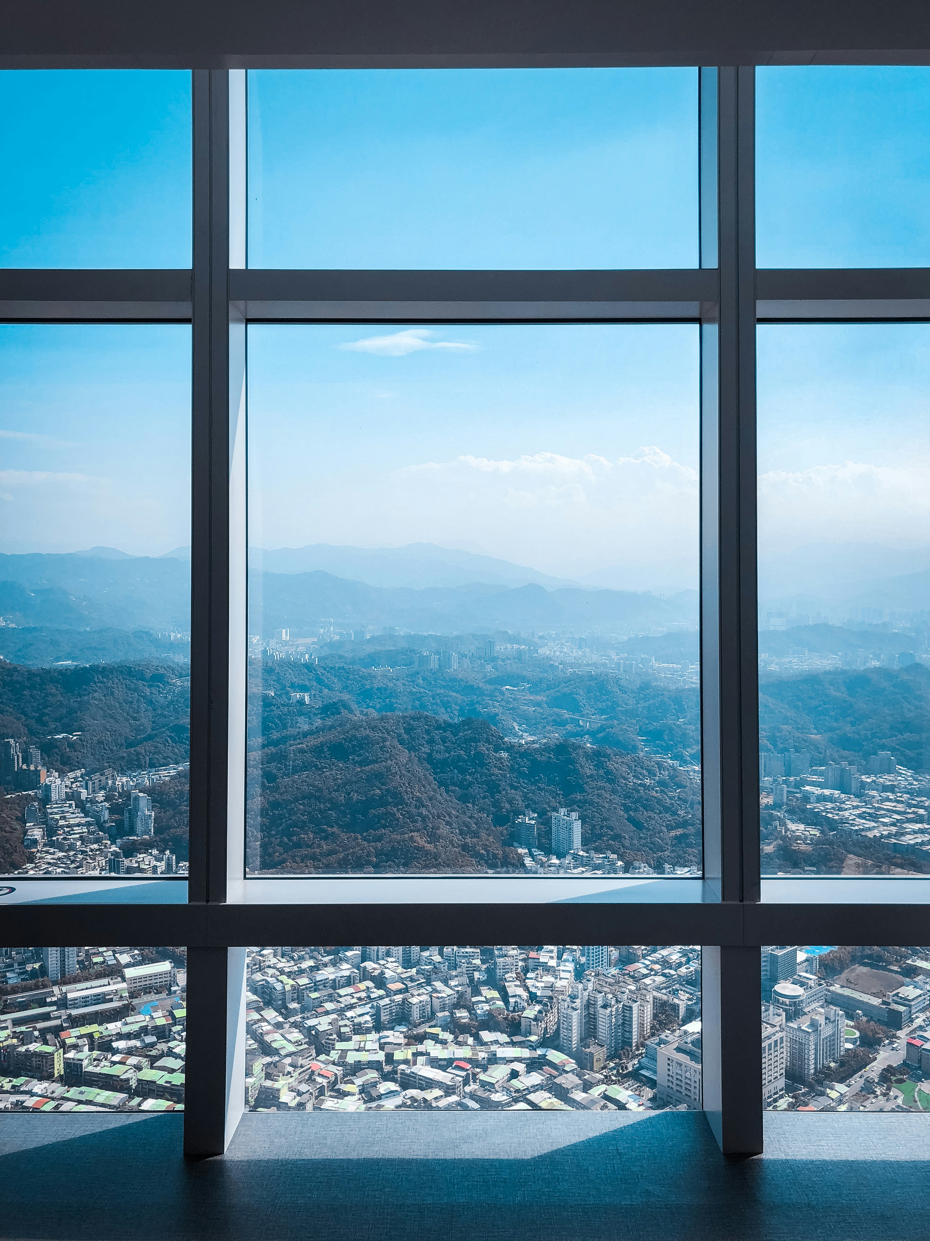 Cityscape view framed by large window panes with distant mountains under a clear blue sky.