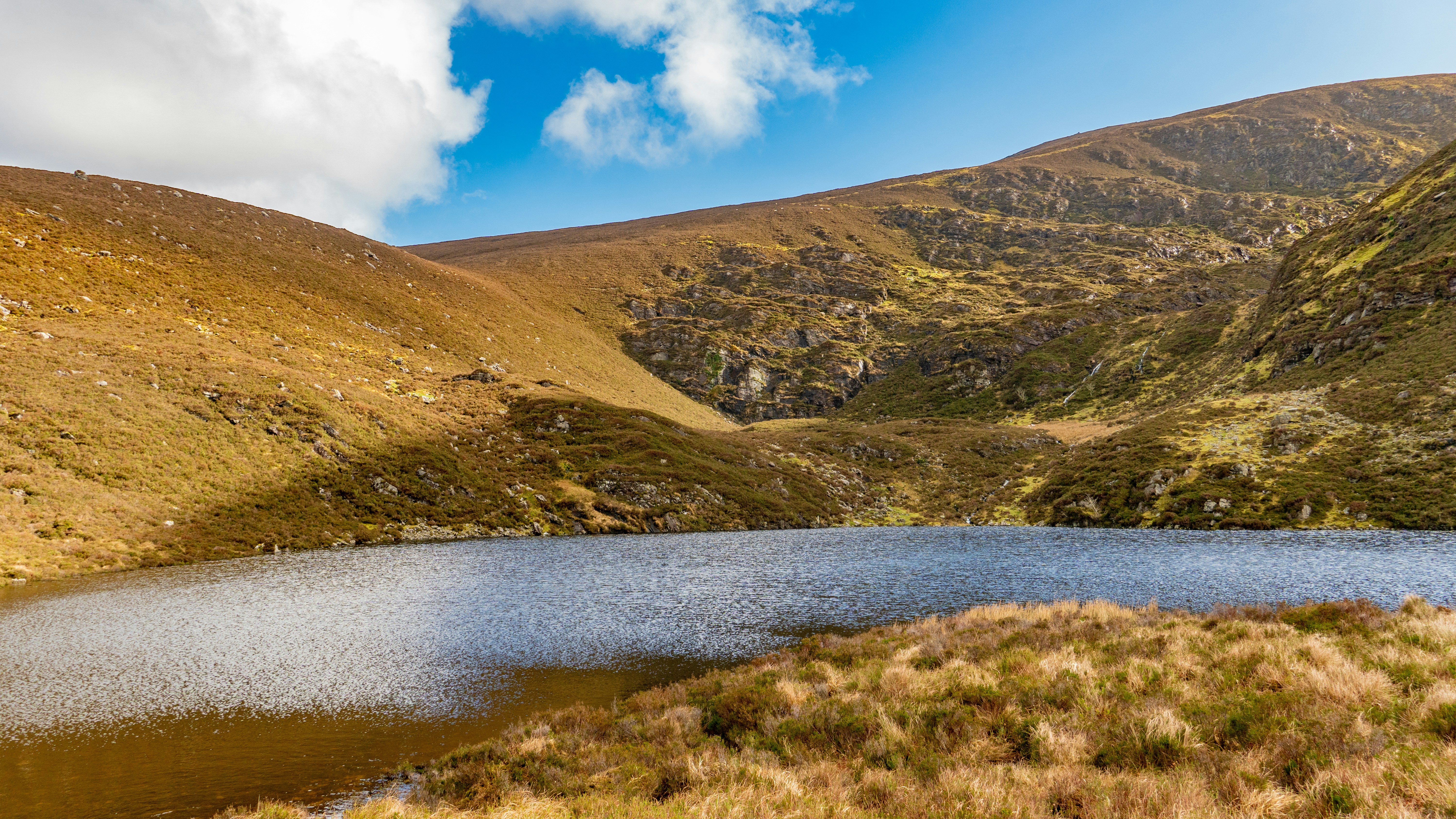 Serene lake nestled among rolling hills under a vibrant blue sky with scattered clouds.