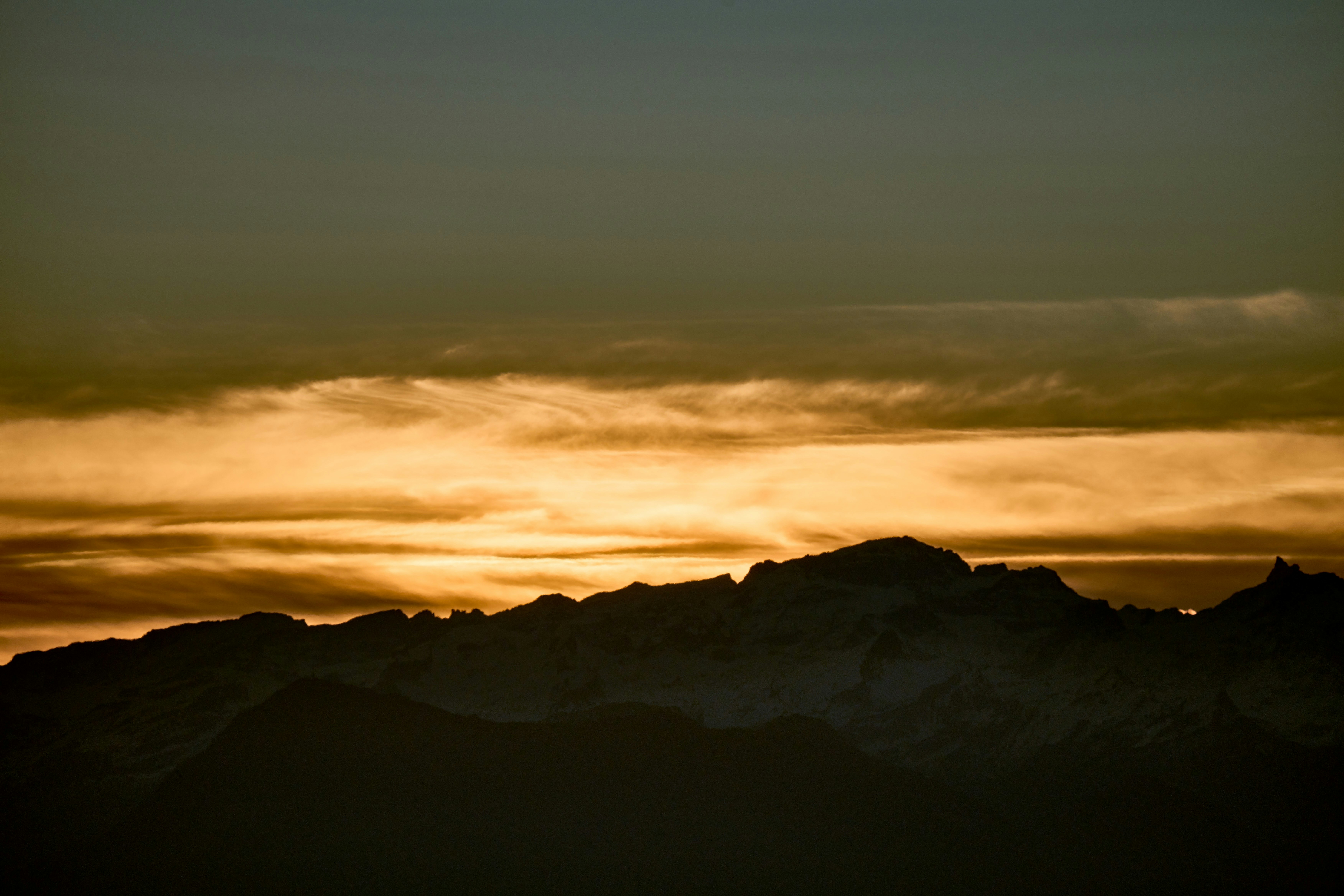 Silhouette of mountain peaks beneath a golden sky at sunset.