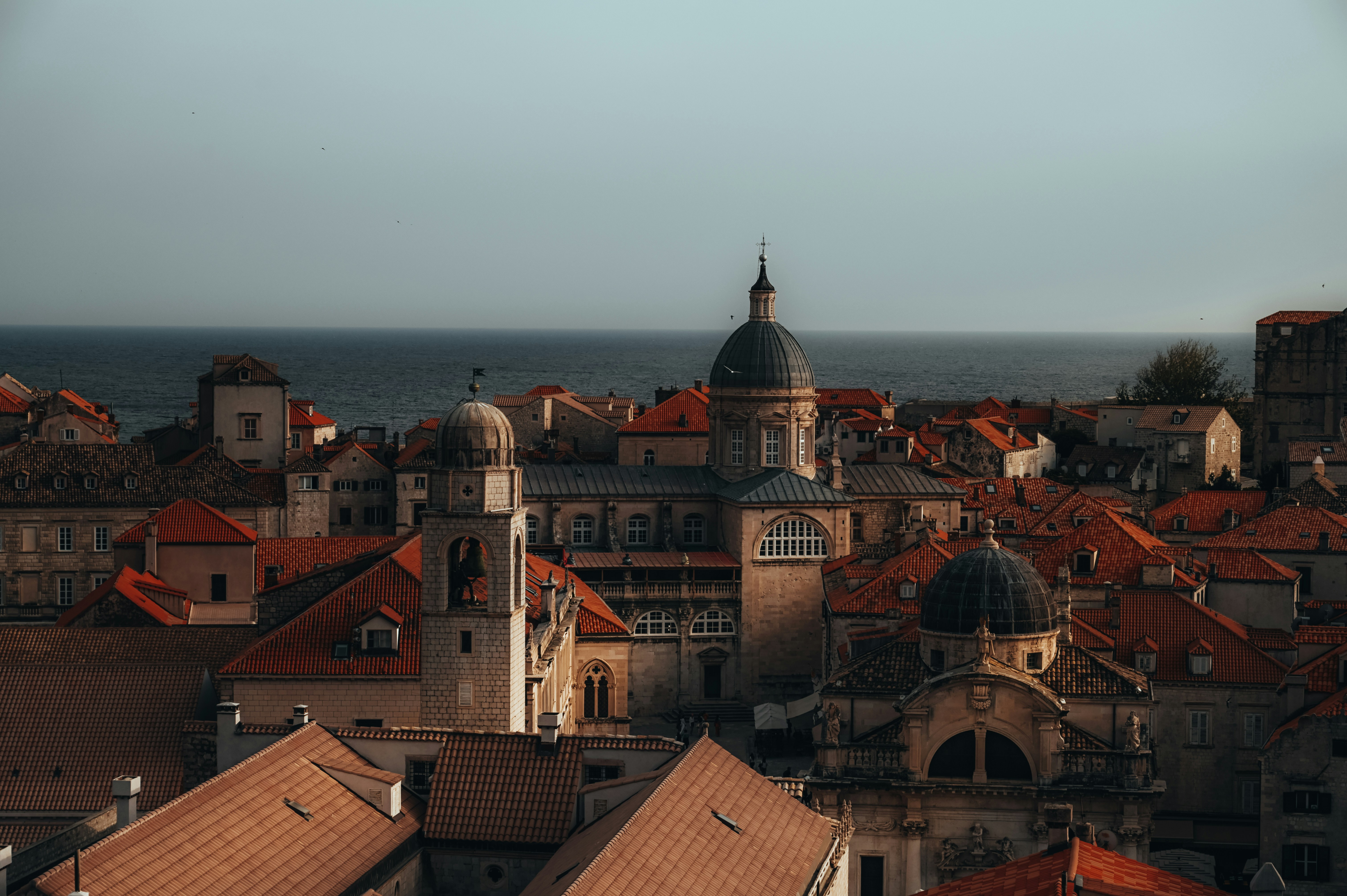 Rooftops and domes overlook the calm, blue sea.