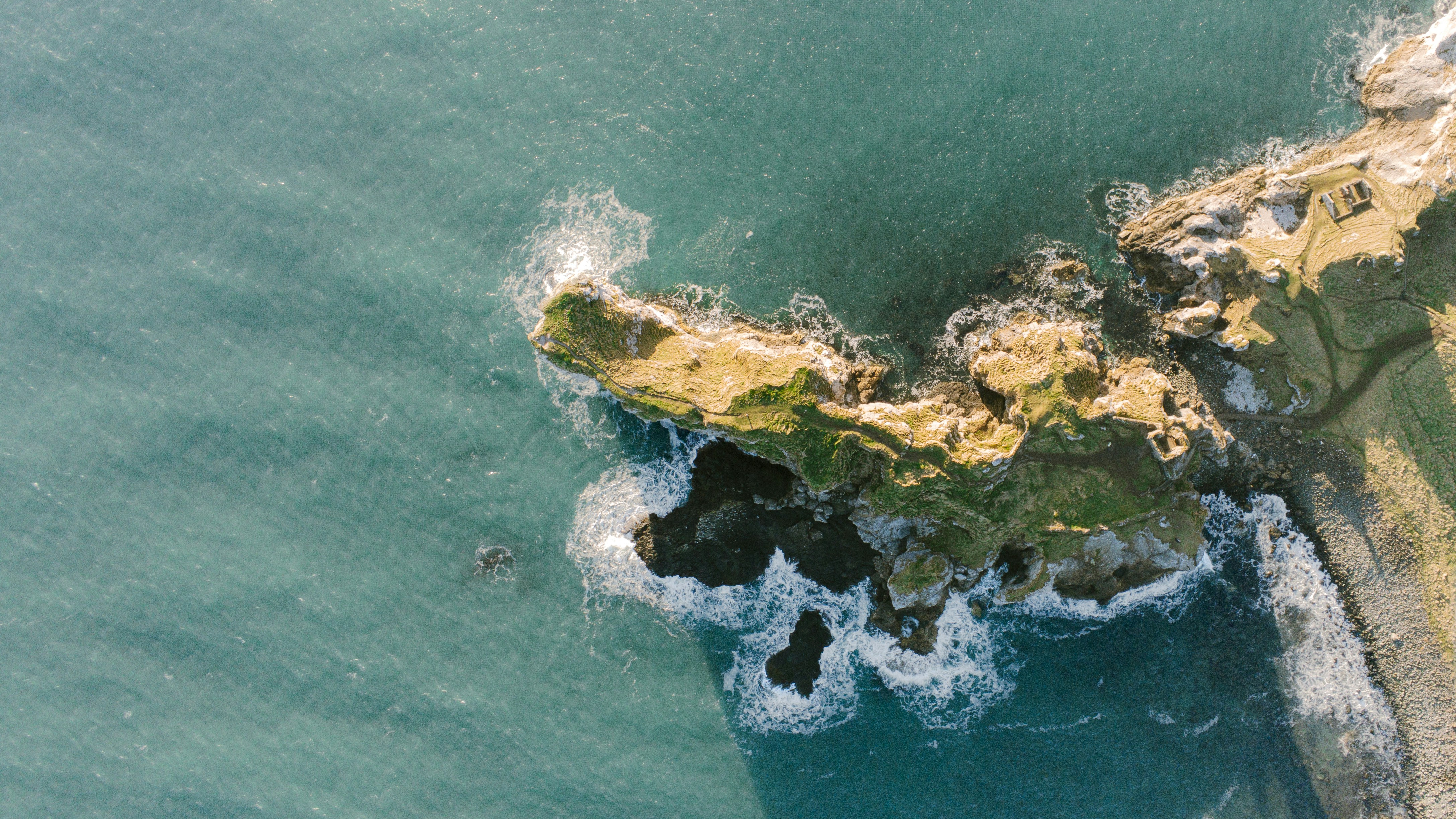 Aerial view of Kinbane Peninsula's rocky outcrop surrounded by swirling ocean waves.