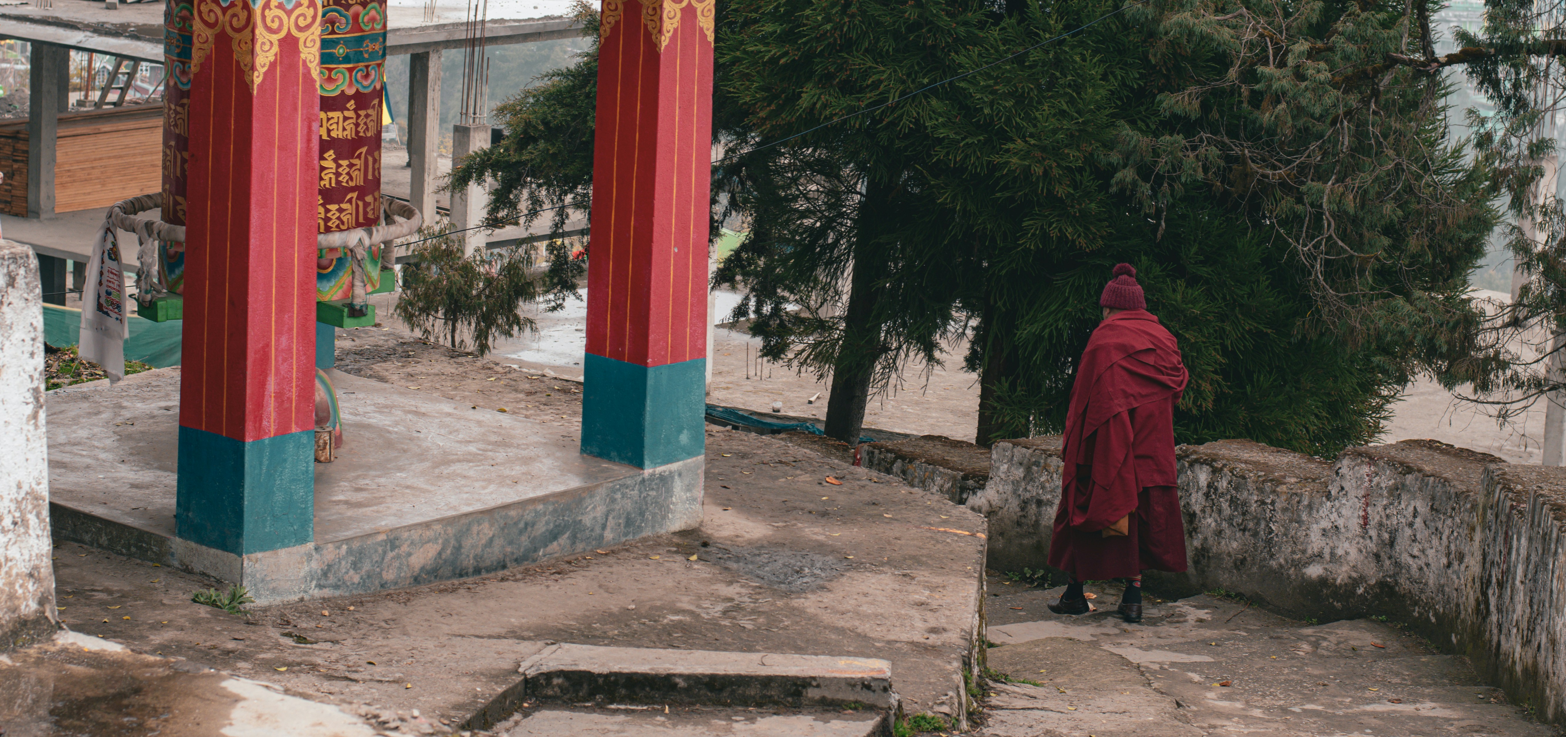 Red-robed monk strides through a sunlit temple courtyard beside vibrant columns