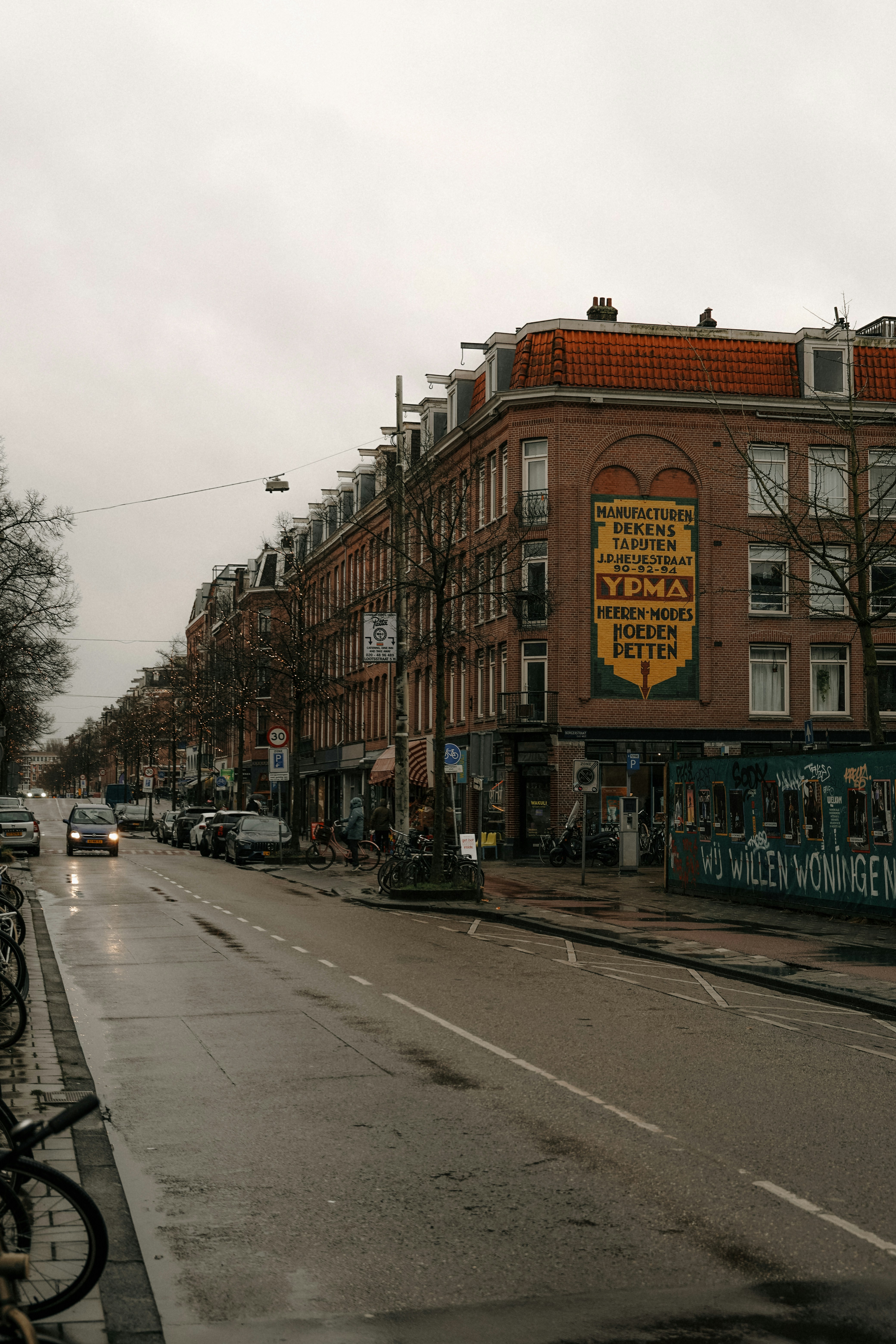 Overcast street scene with wet pavement and a row of brick buildings under a cloudy sky.