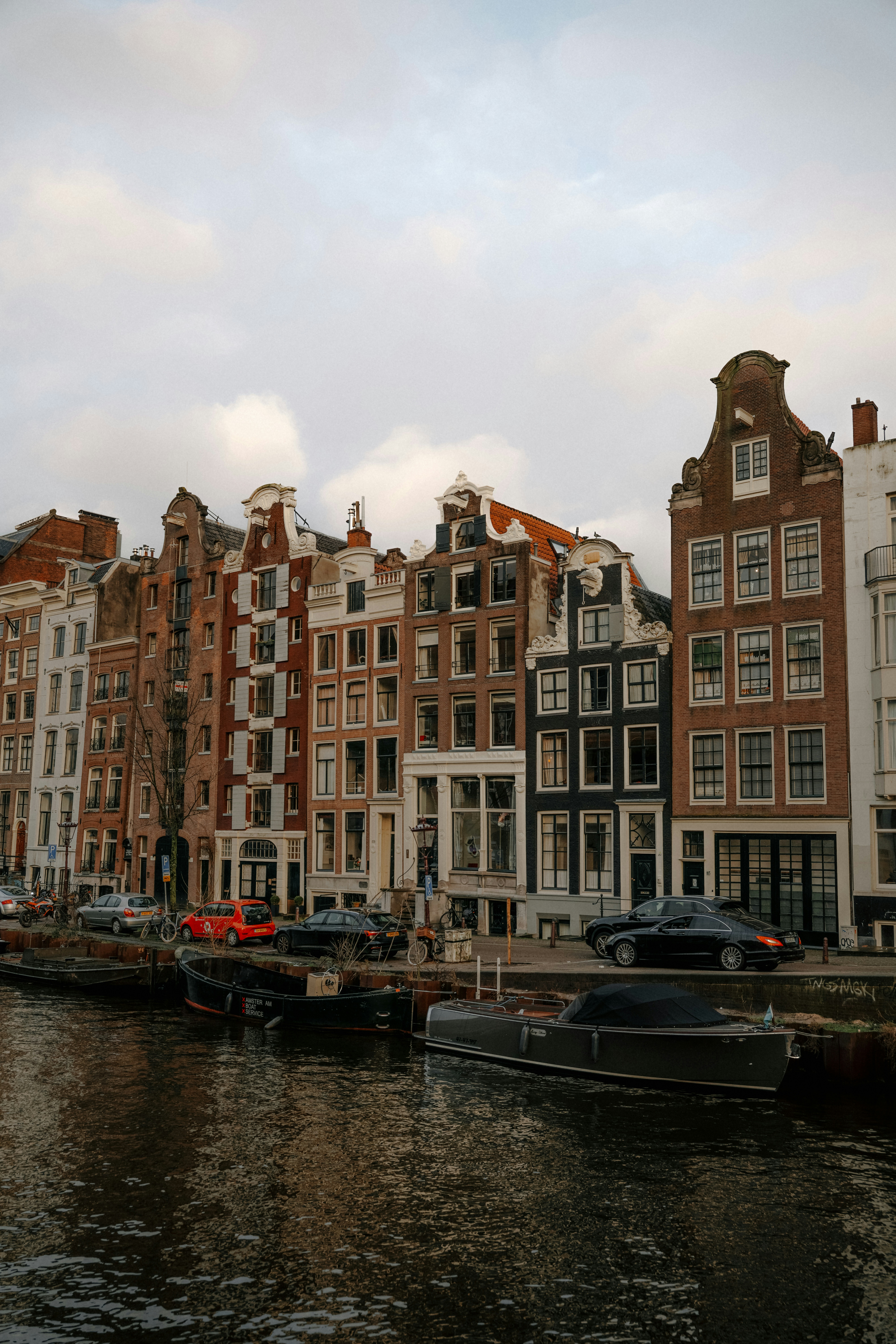 Row of historic buildings alongside a tranquil canal under a cloudy sky.