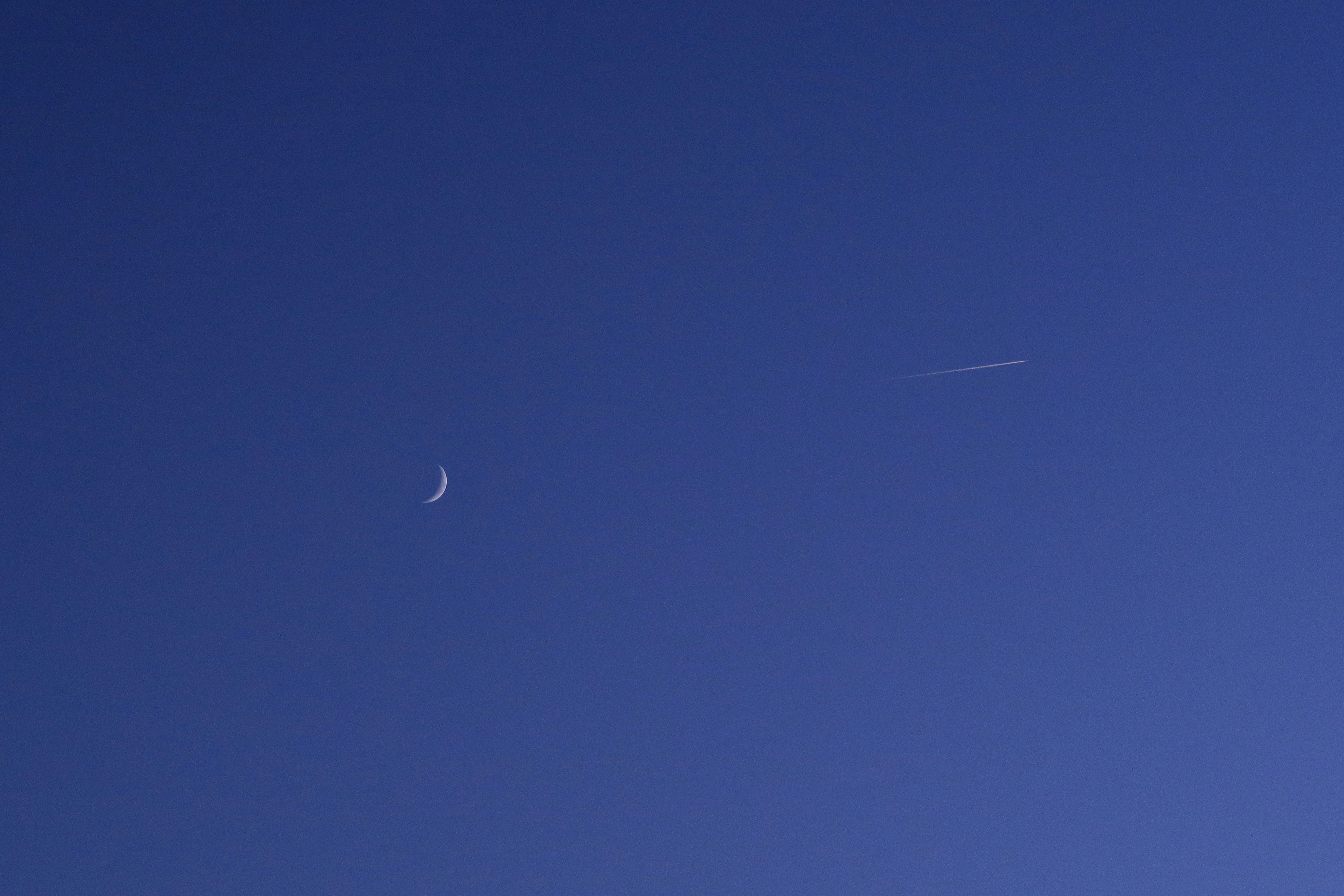 Crescent moon and a satellite trail against a deep blue evening sky.